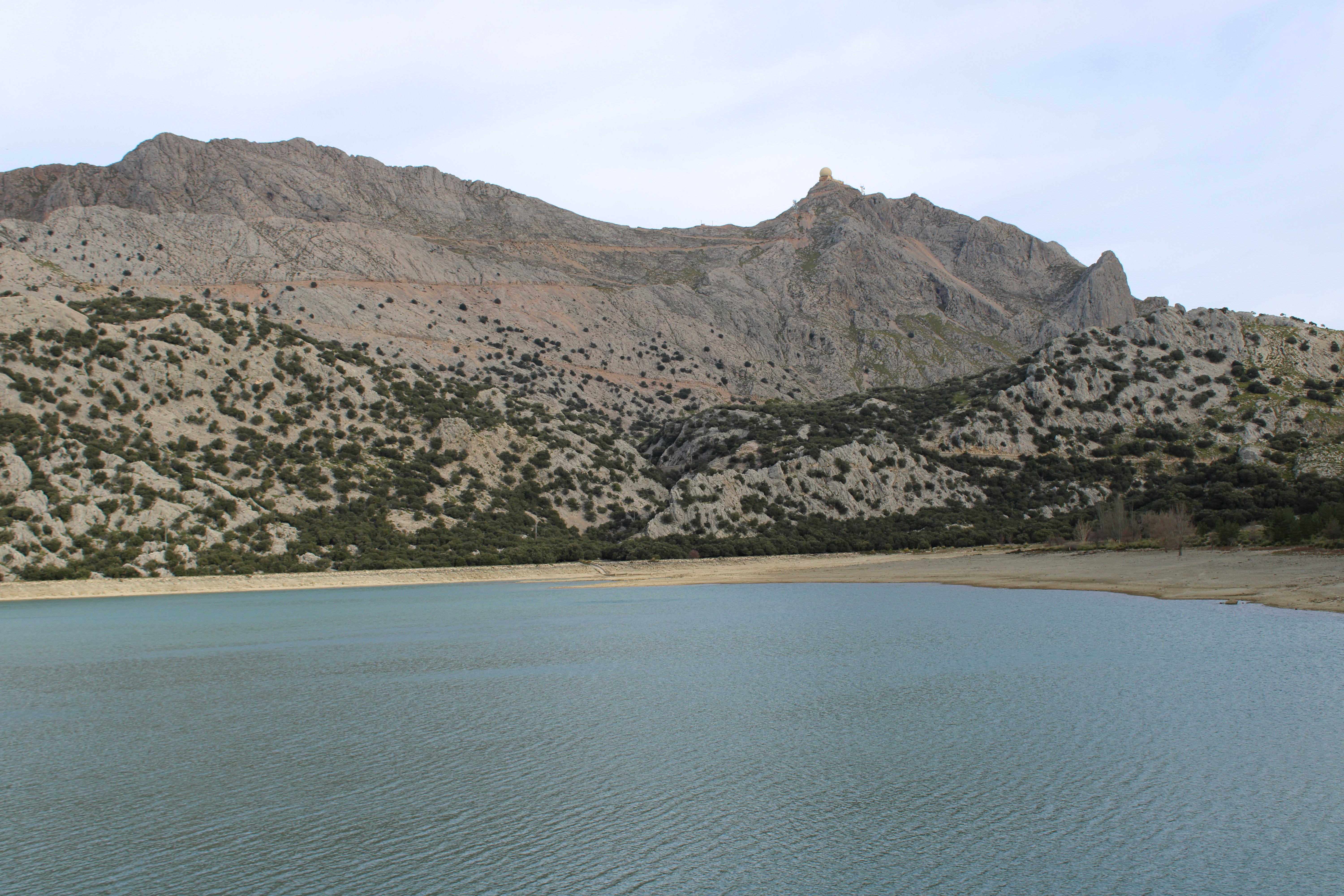 Lago | A lake reflects mountains under cloudy skies.