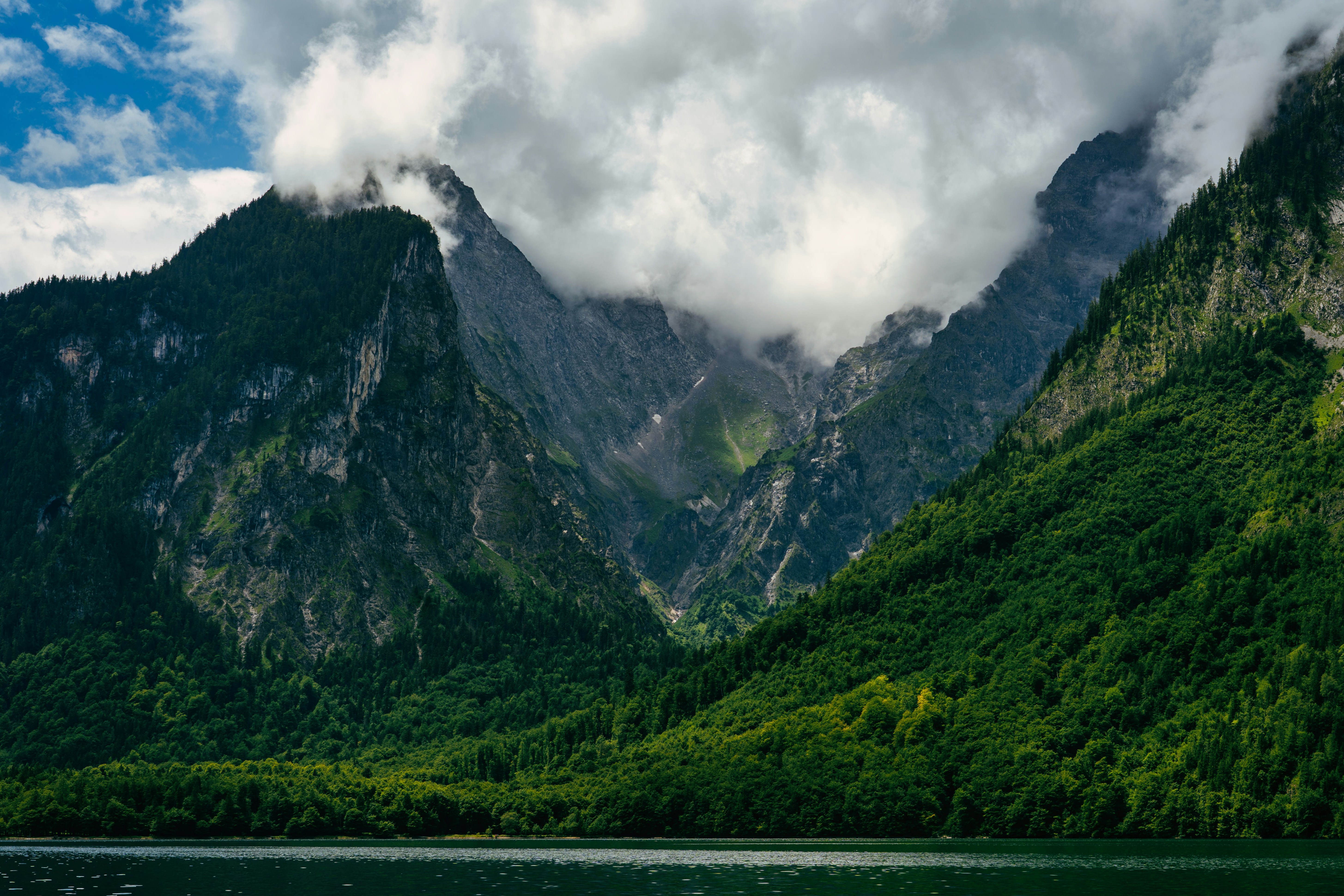 Königsee | Green mountains peak under cloudy skies.