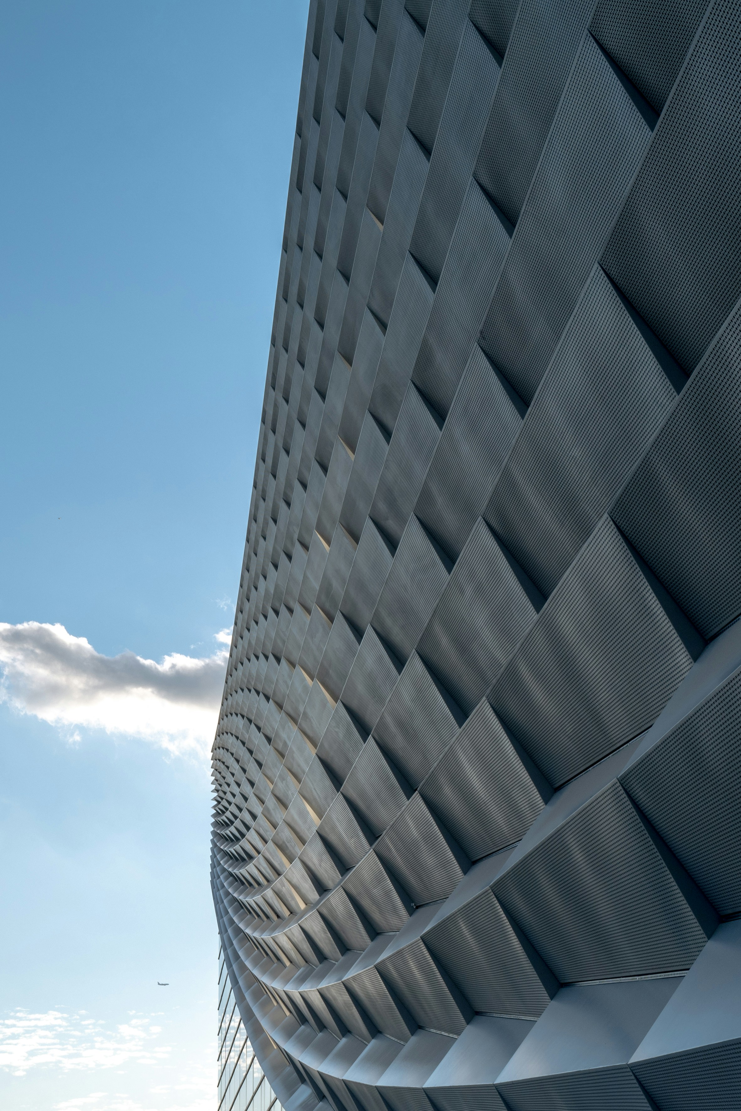Curved metallic façade of a contemporary building against a clear blue sky, showcasing intricate geometric patterns.