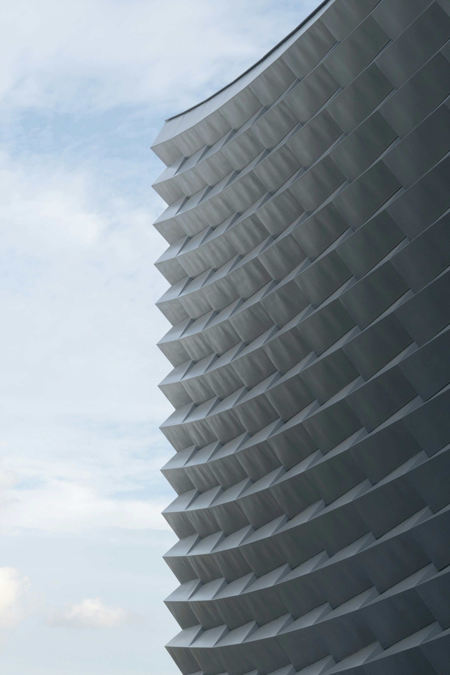 A sweeping curve of metal panels on the facade of the Beijing Performing Arts Center in Tongzhou, Beijing. The repeating geometric rhythm against a pale sky reflects the minimal elegance of modern Chinese architecture. | A modern building with a unique facade.