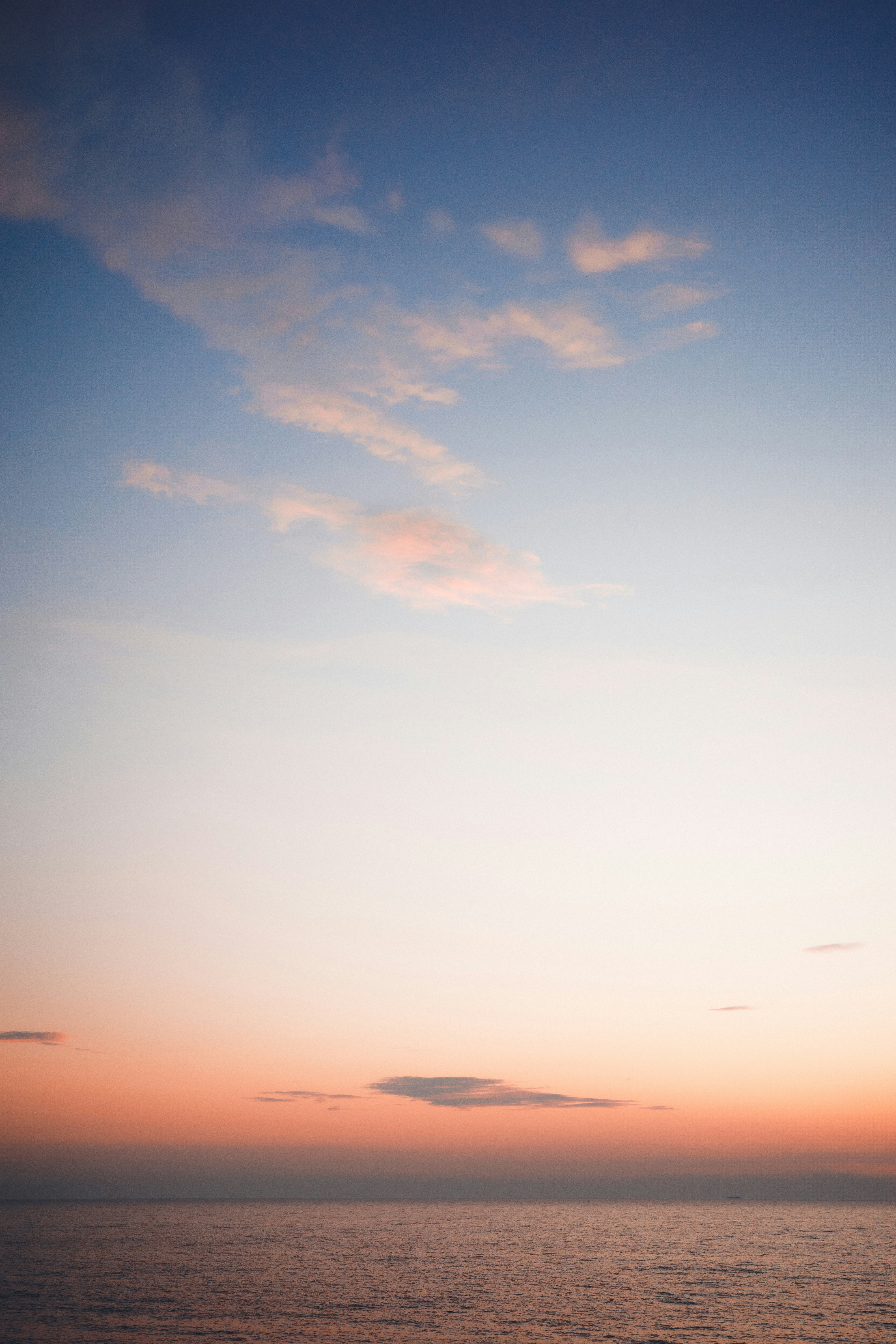Soft pastel hues blend in the sky above a calm sea, with wispy clouds reflecting the day's end. A serene moment captured in nature's embrace.