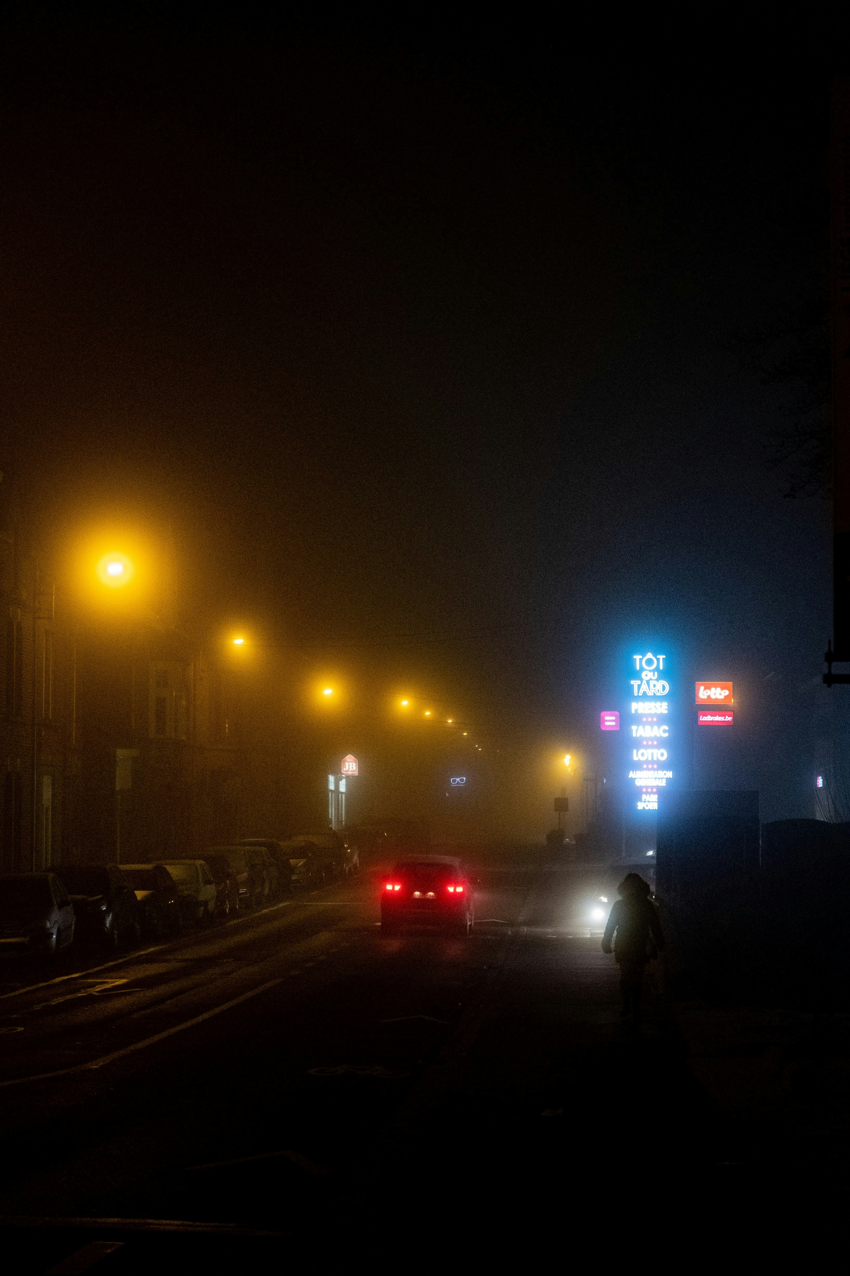 A foggy night street with cars and lights.