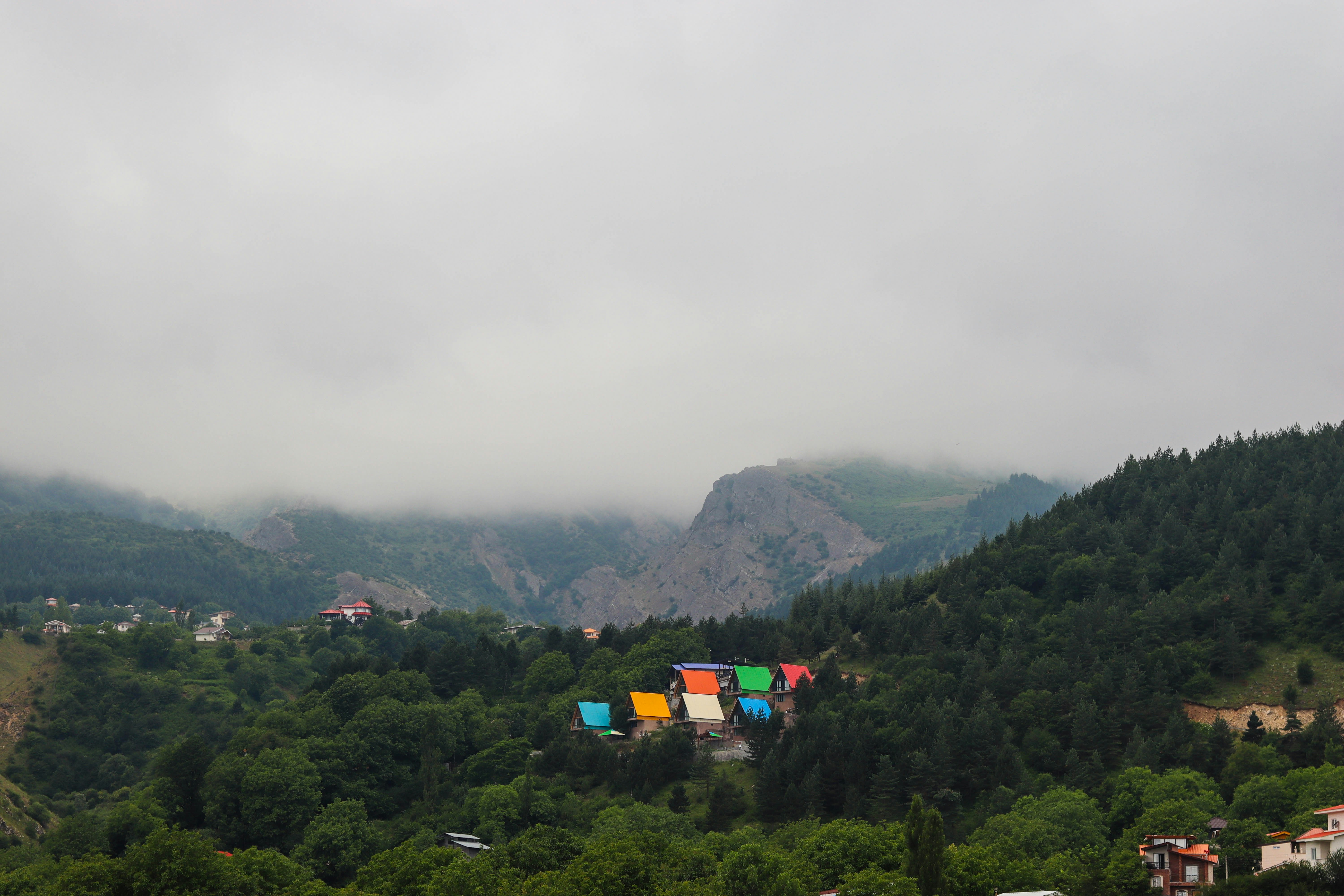Vibrant houses with colorful roofs nestled in a lush valley, surrounded by misty mountains and dense greenery.