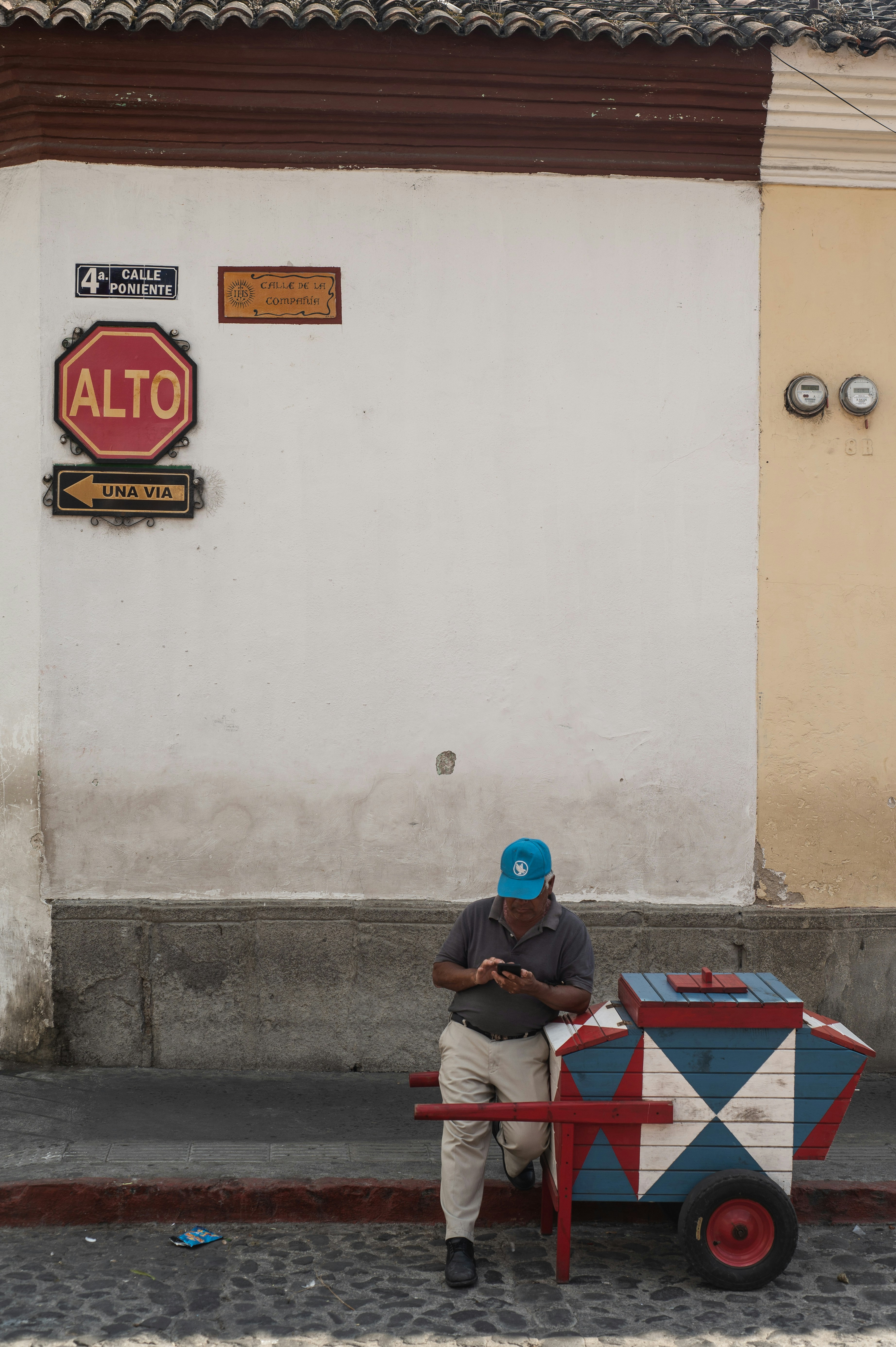 A man sits beside his cart, using his phone.