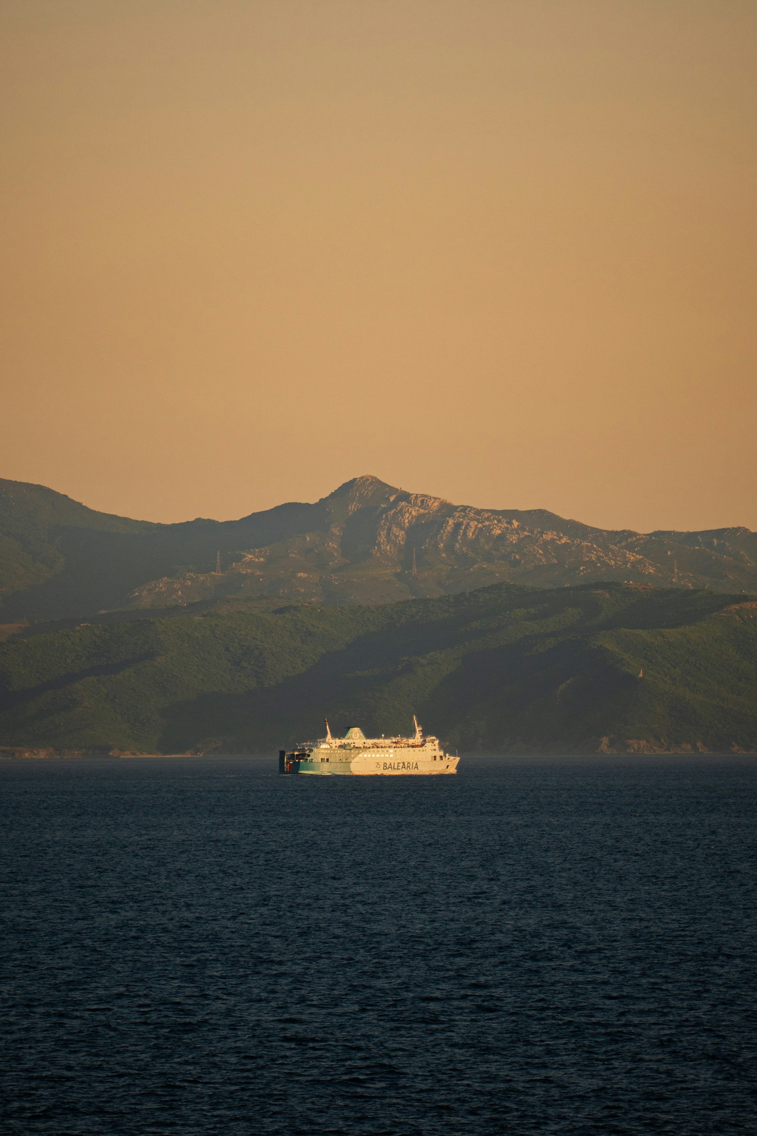 A ferry gliding across calm waters with distant mountains silhouetted against a warm evening sky.