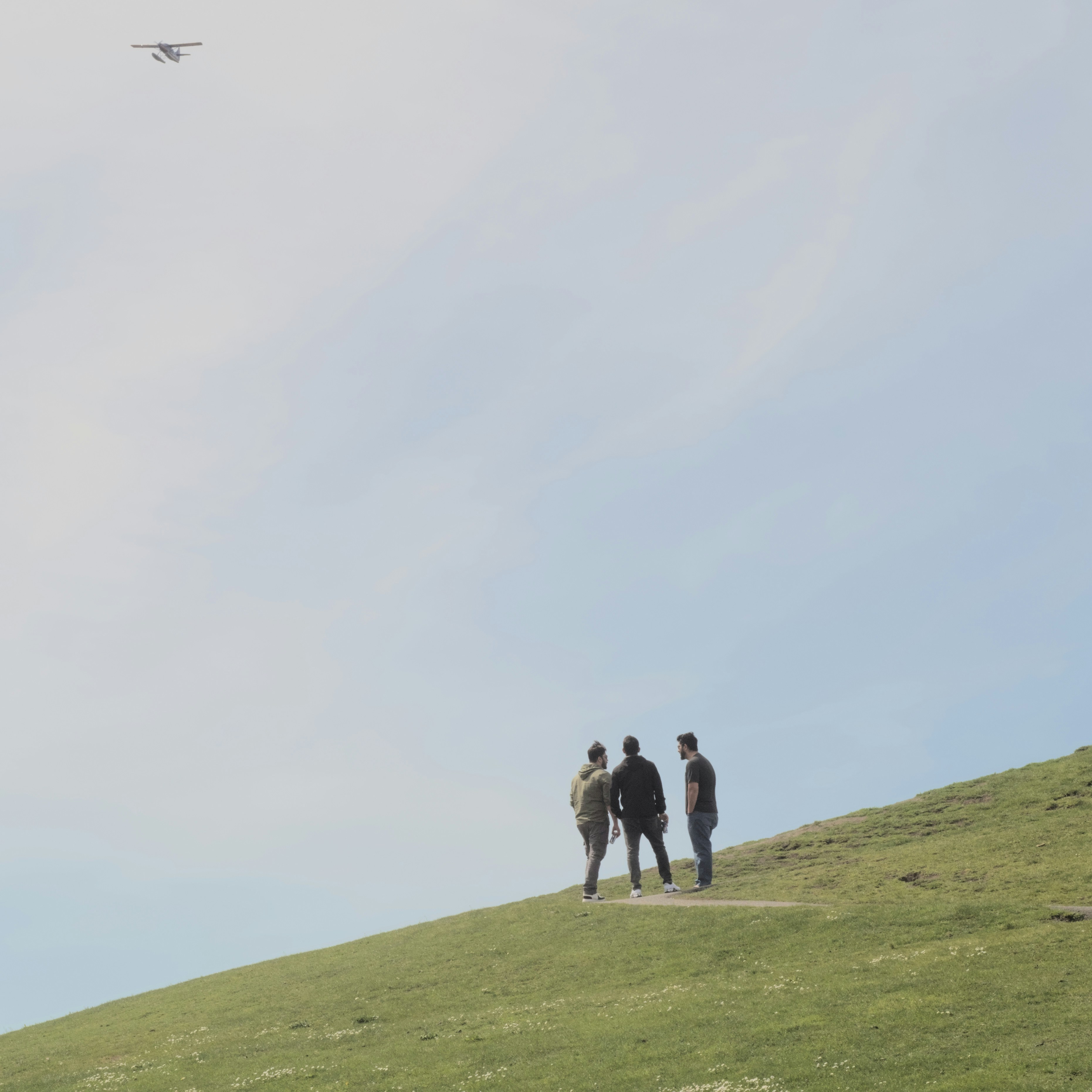 Fuji XT2 + Olympus Zuiko 135mm 3.5 | People are watching a plane fly over a hill.