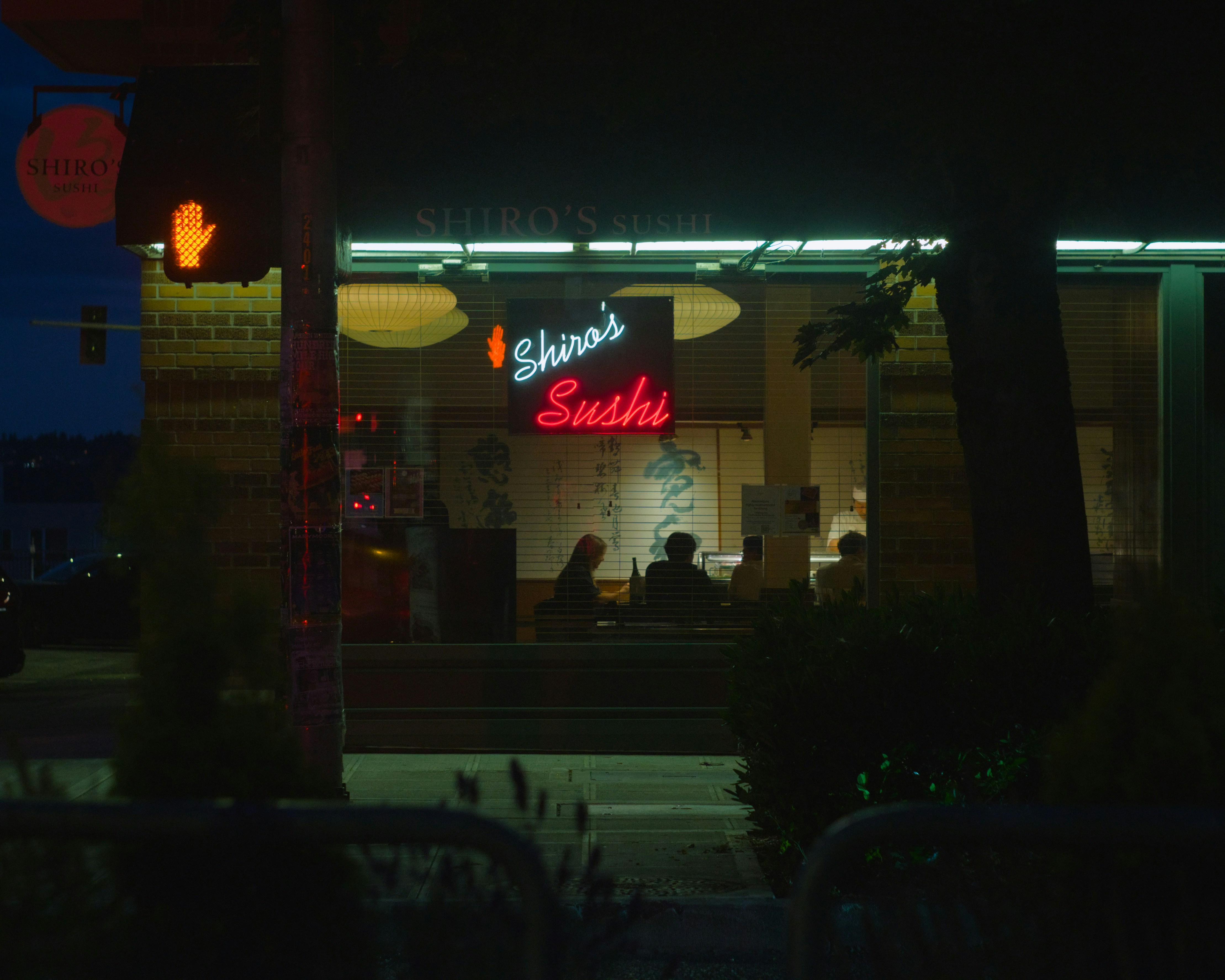 Illuminated neon sign of Shiro's Sushi glows against the night, inviting diners inside. The warm ambiance contrasts with the dark surroundings.