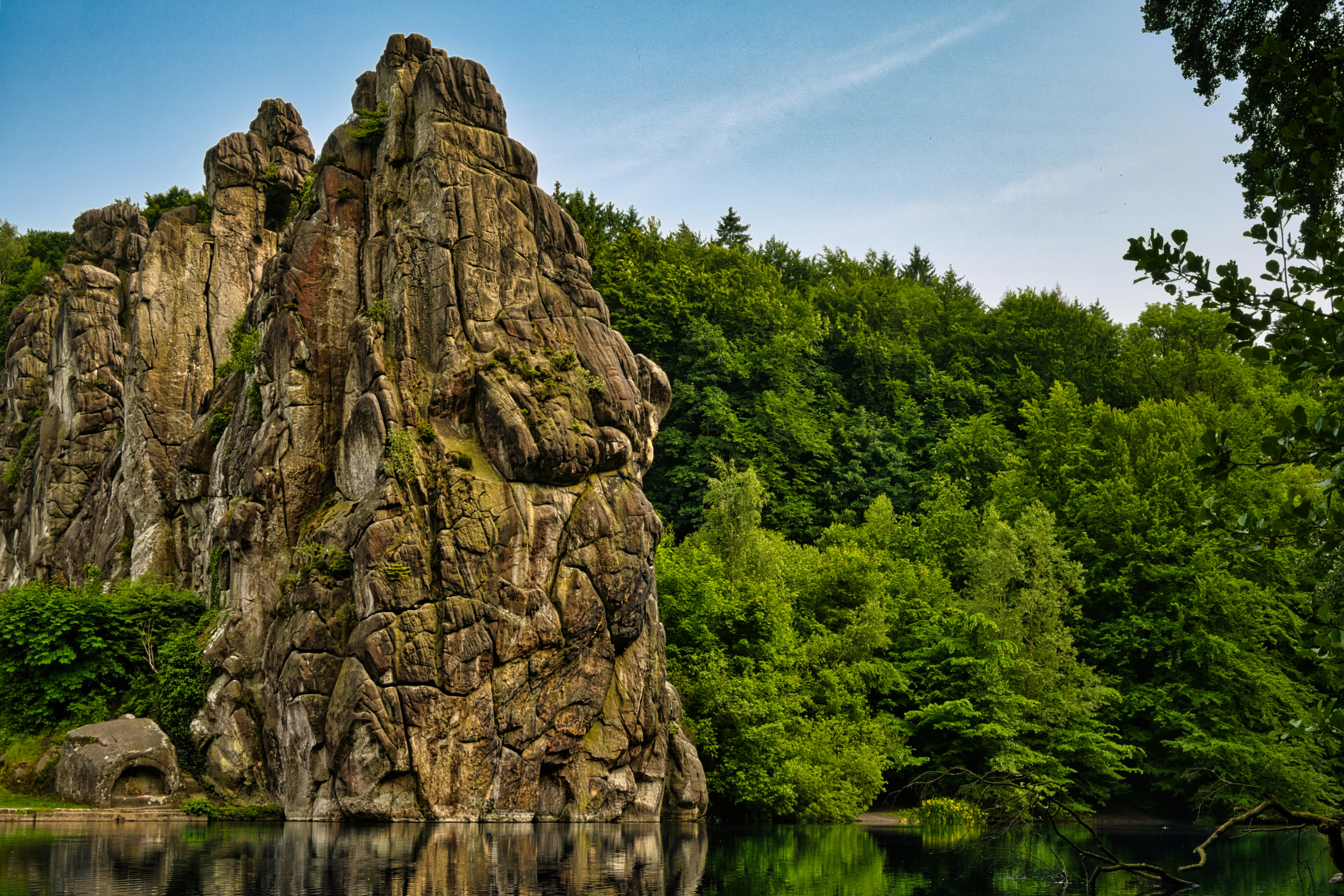 Majestic rock formation rising above a serene lake, surrounded by lush greenery and reflecting in the calm water.