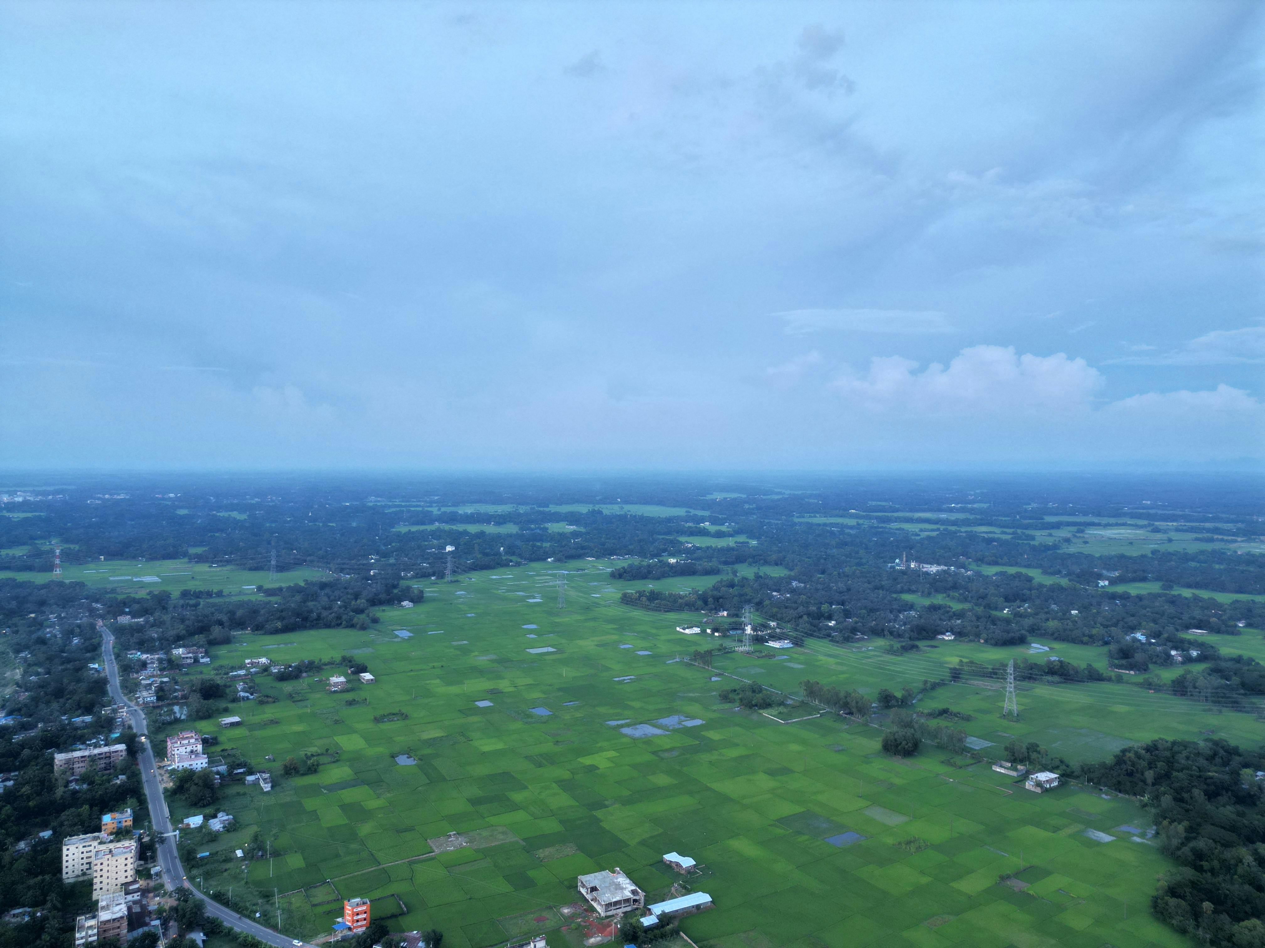Aerial View of Green Paddy Fields and Countryside Under a Cloudy Sky | Overhead view of lush green fields and blue skies.