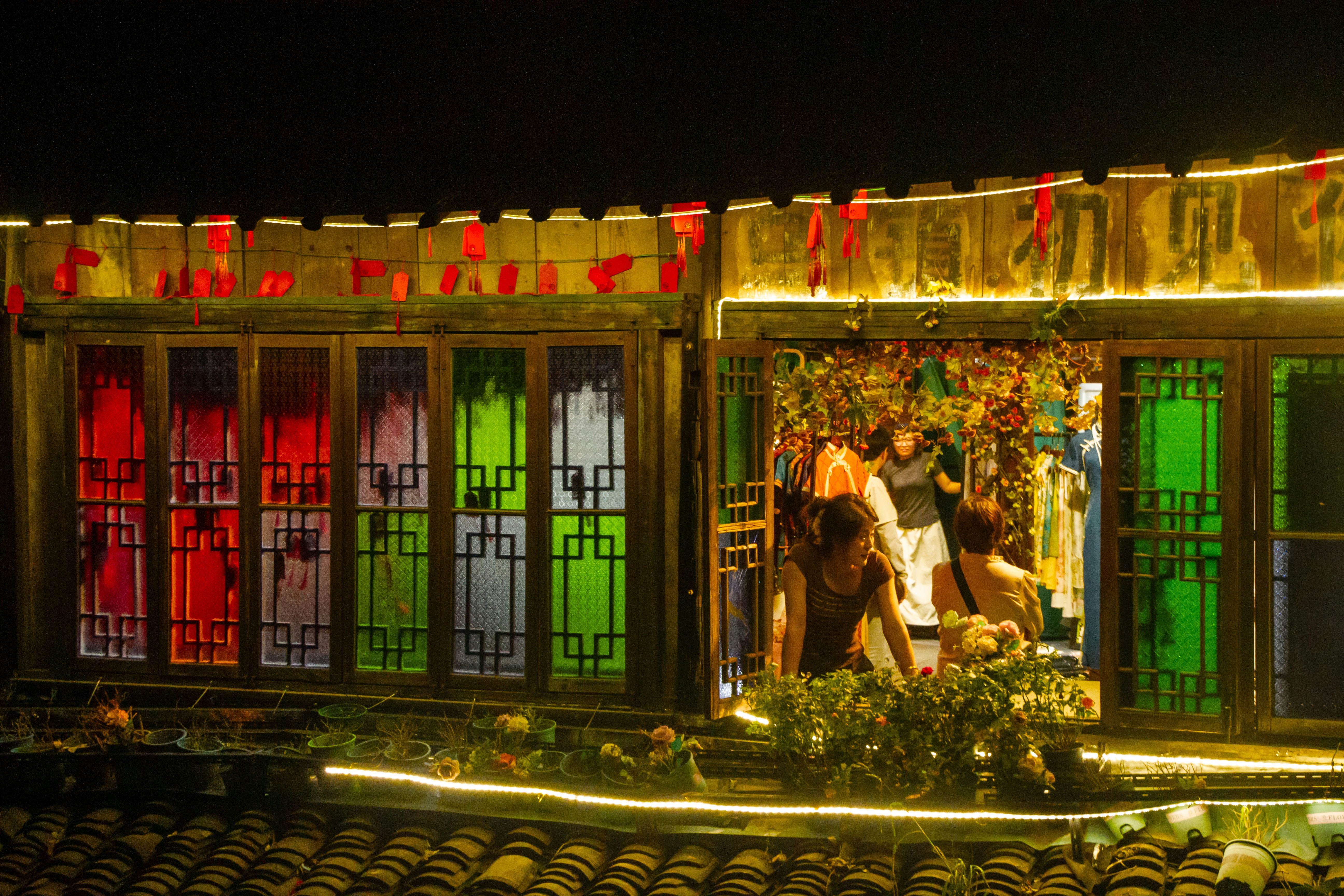 A house near a night market. | A brightly lit store with colorful windows at night.