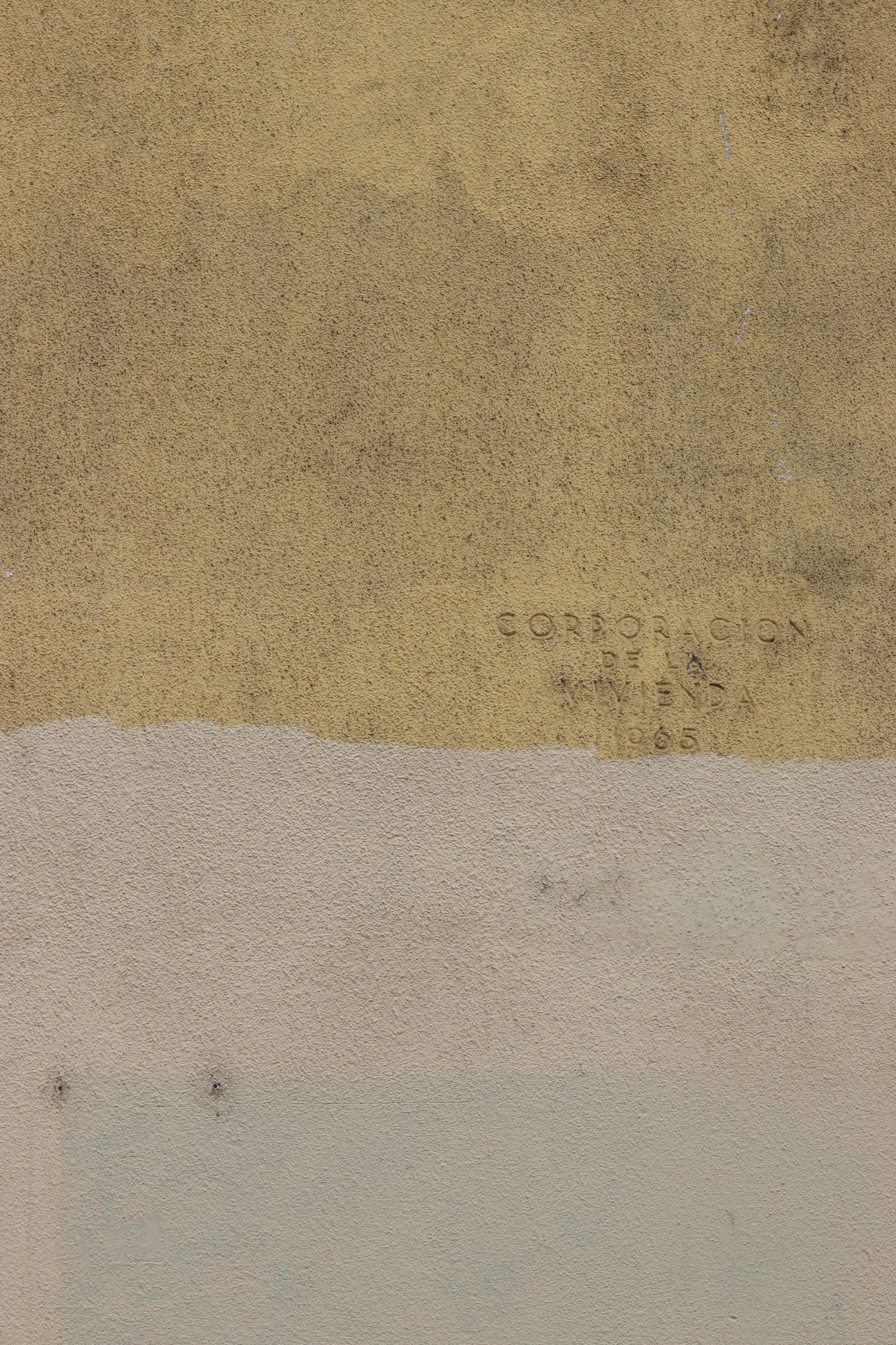 Faded yellow wall with subtle texture and an inscription reading 'CORPORACION DE A. M. B. R. A. 1865.'