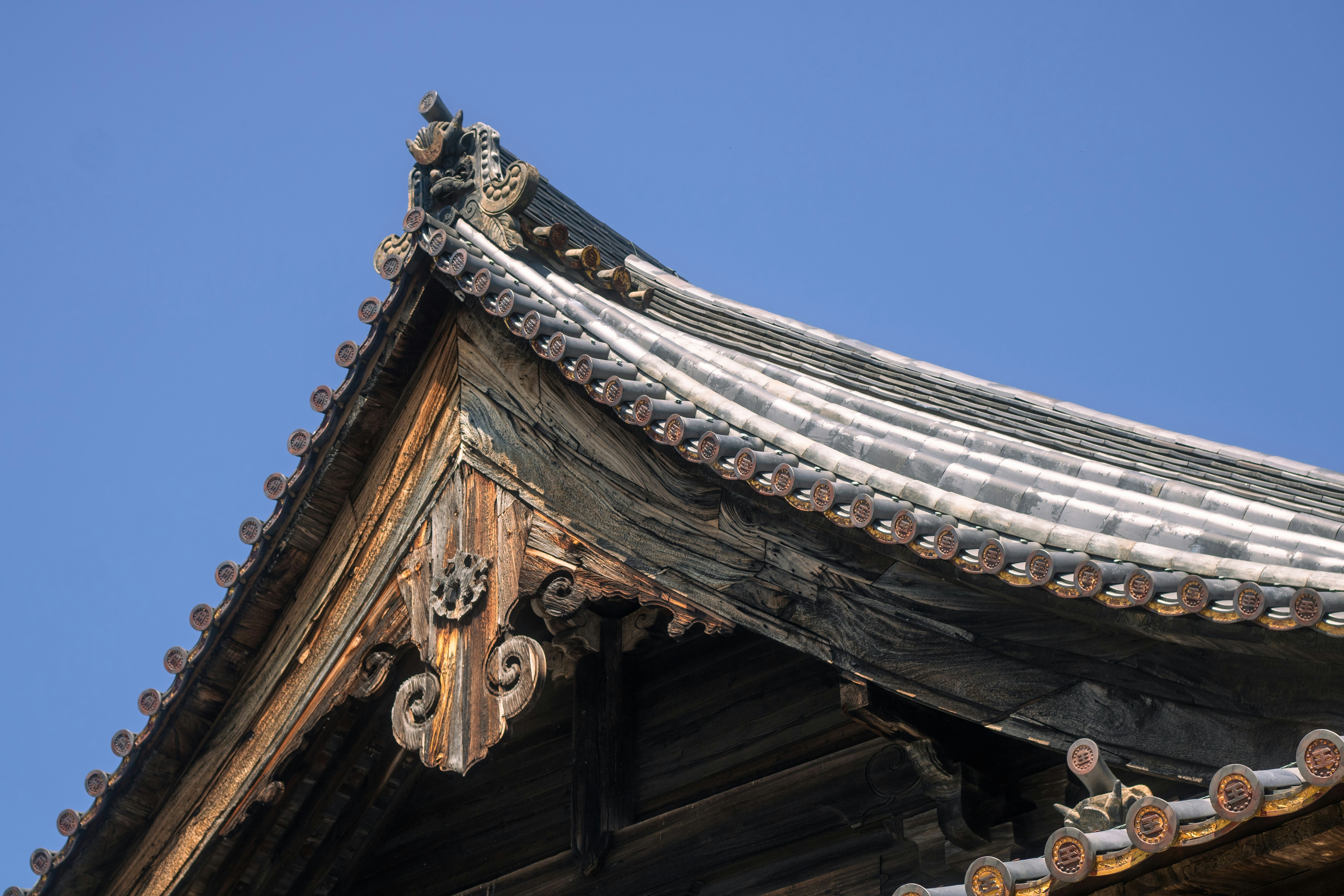 Intricate wooden eaves of a traditional structure against a clear blue sky. The craftsmanship showcases historical architectural details.