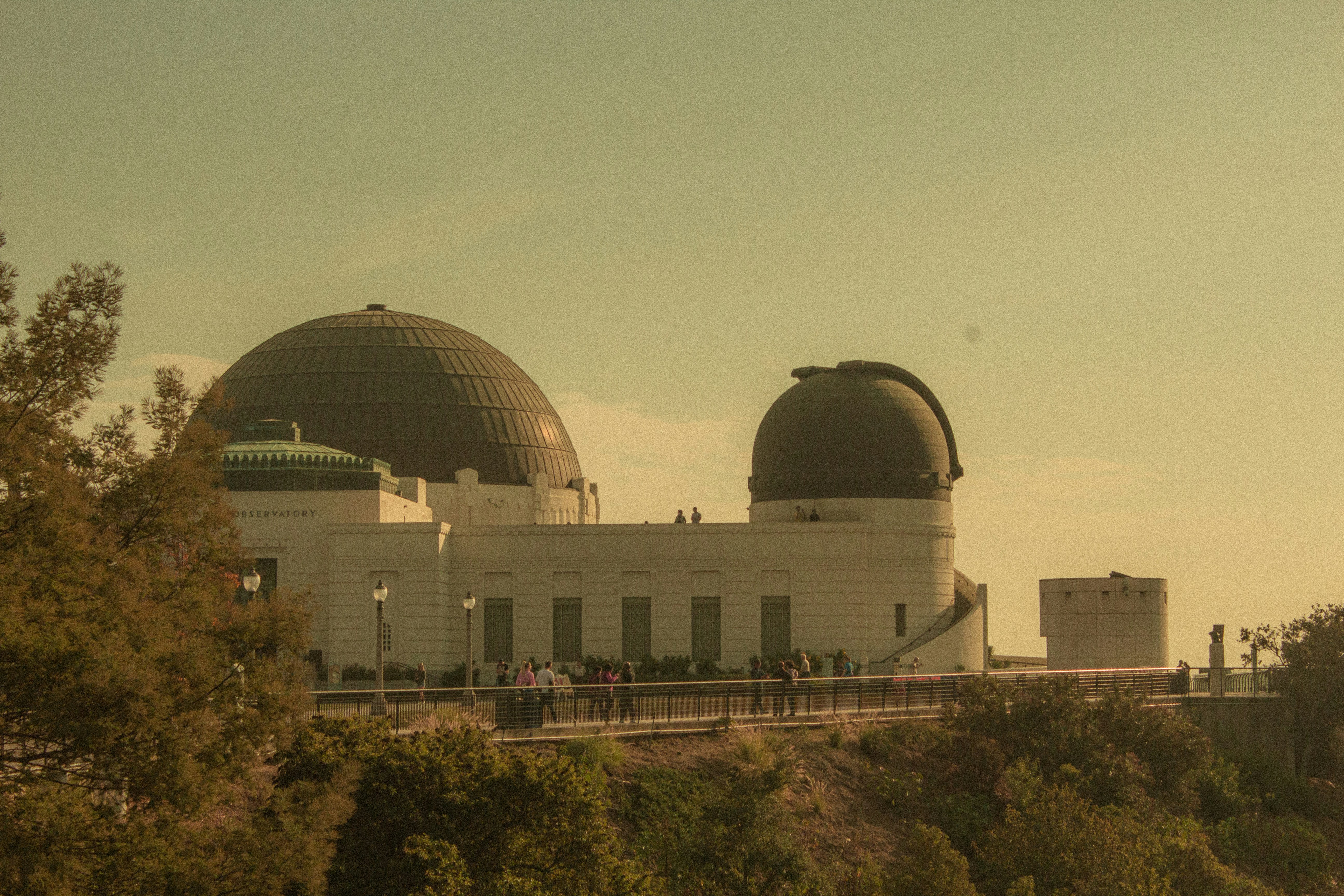 Historic observatory perched on a hillside, showcasing its iconic domes against a hazy sky. Visitors gather, drawn by the allure of the cosmos.
