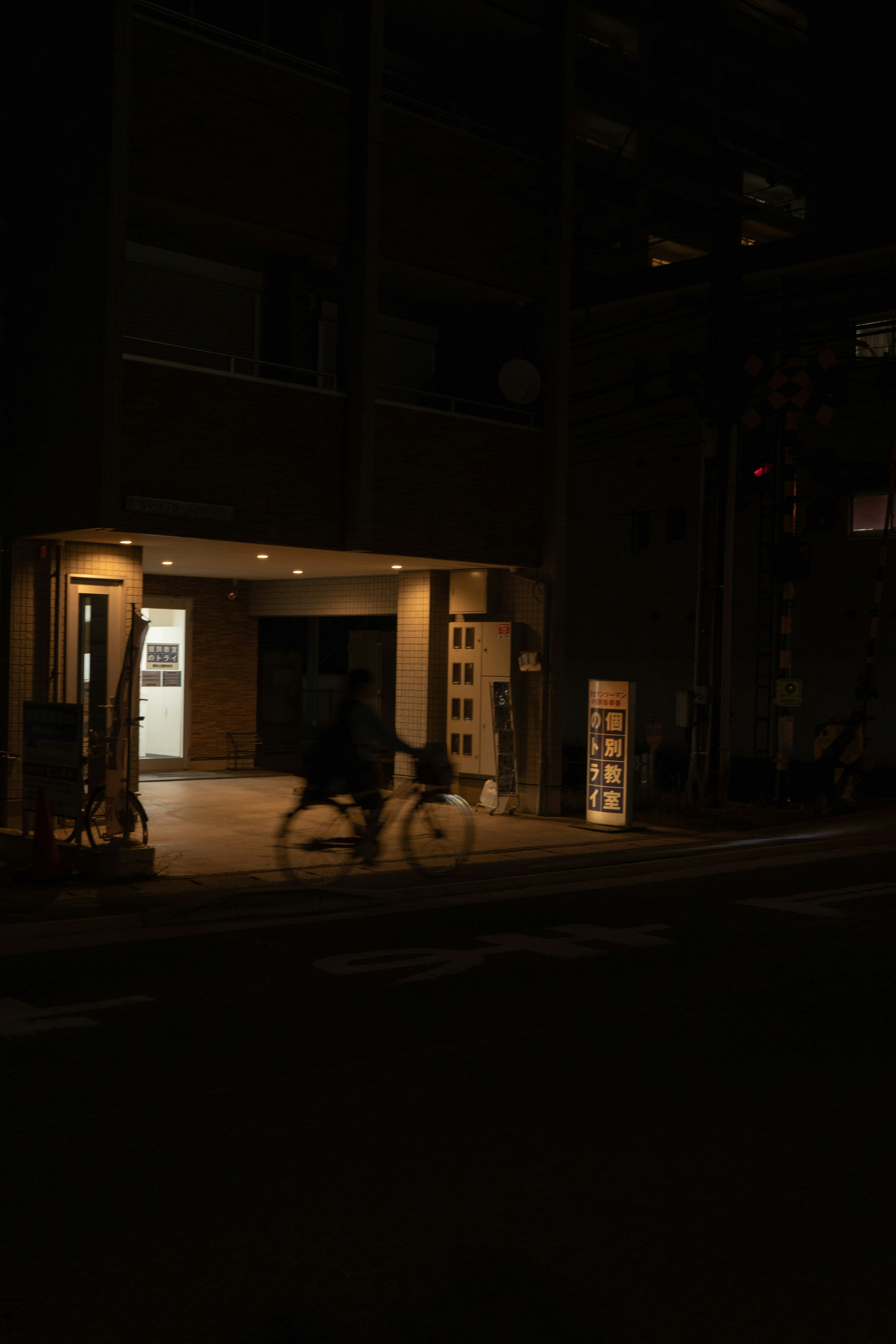 A cyclist rides past a building at night.
