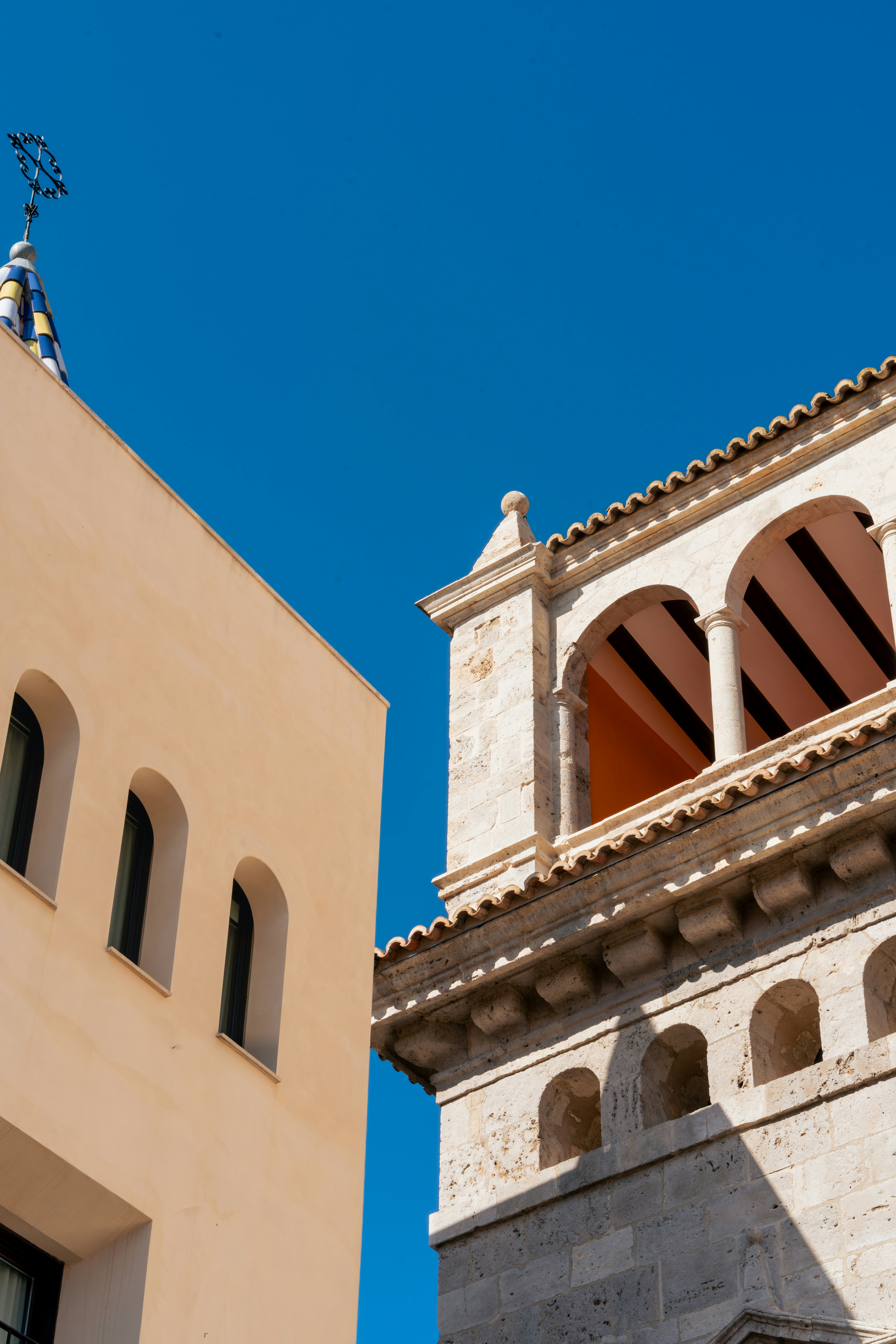 Historic stone building with arched windows juxtaposed against a modern light-colored structure under a clear blue sky.