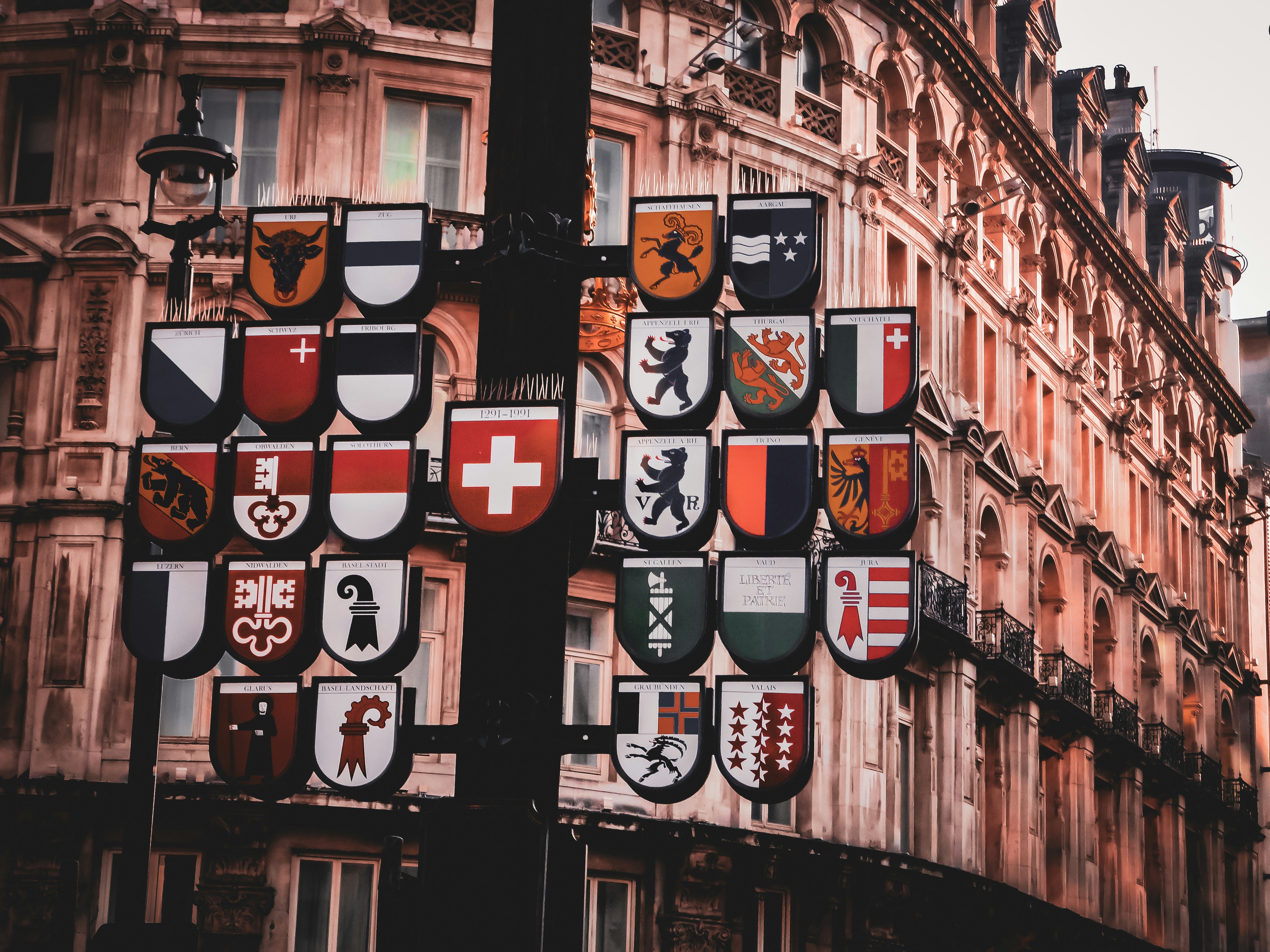 Signs displaying coats of arms hang on a lamppost.