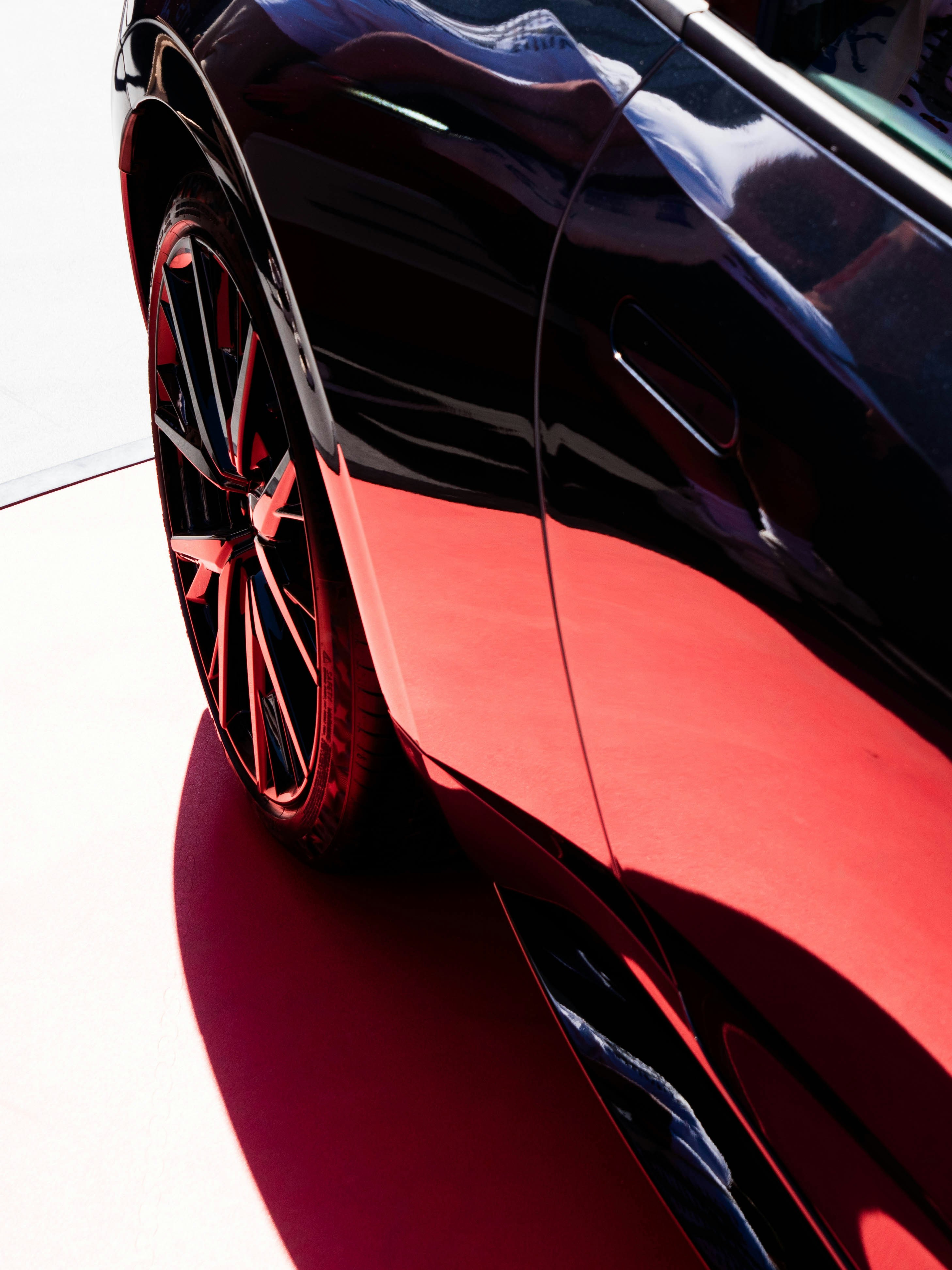 A colourful pink and black photo of a Rolls Royce rear wheel. | A sleek, black car reflected in red light.
