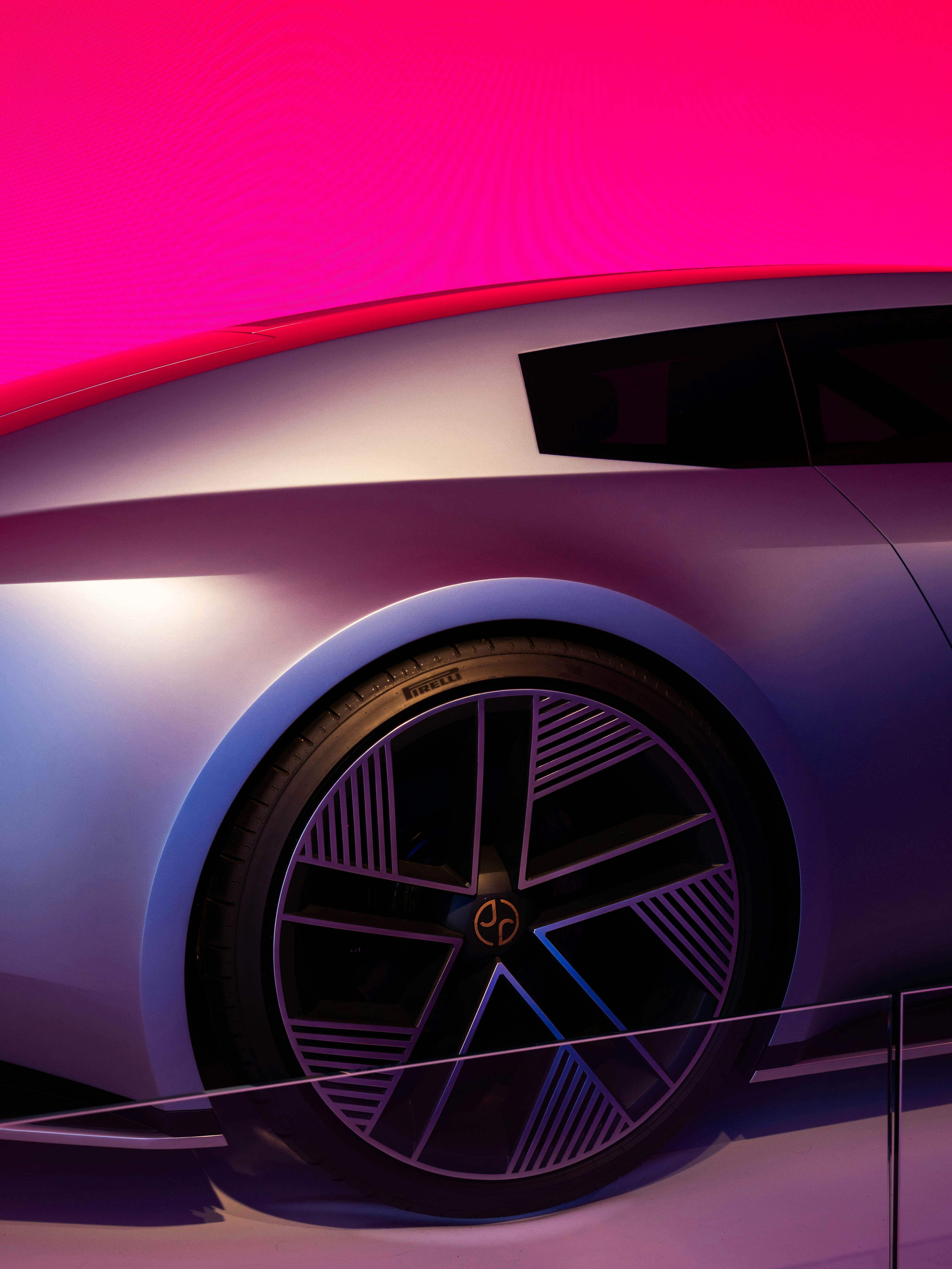 The rear wheel of a silver concept Jaguar car on a pink background. | Here's a caption: a sleek, modern car's wheel and body.
