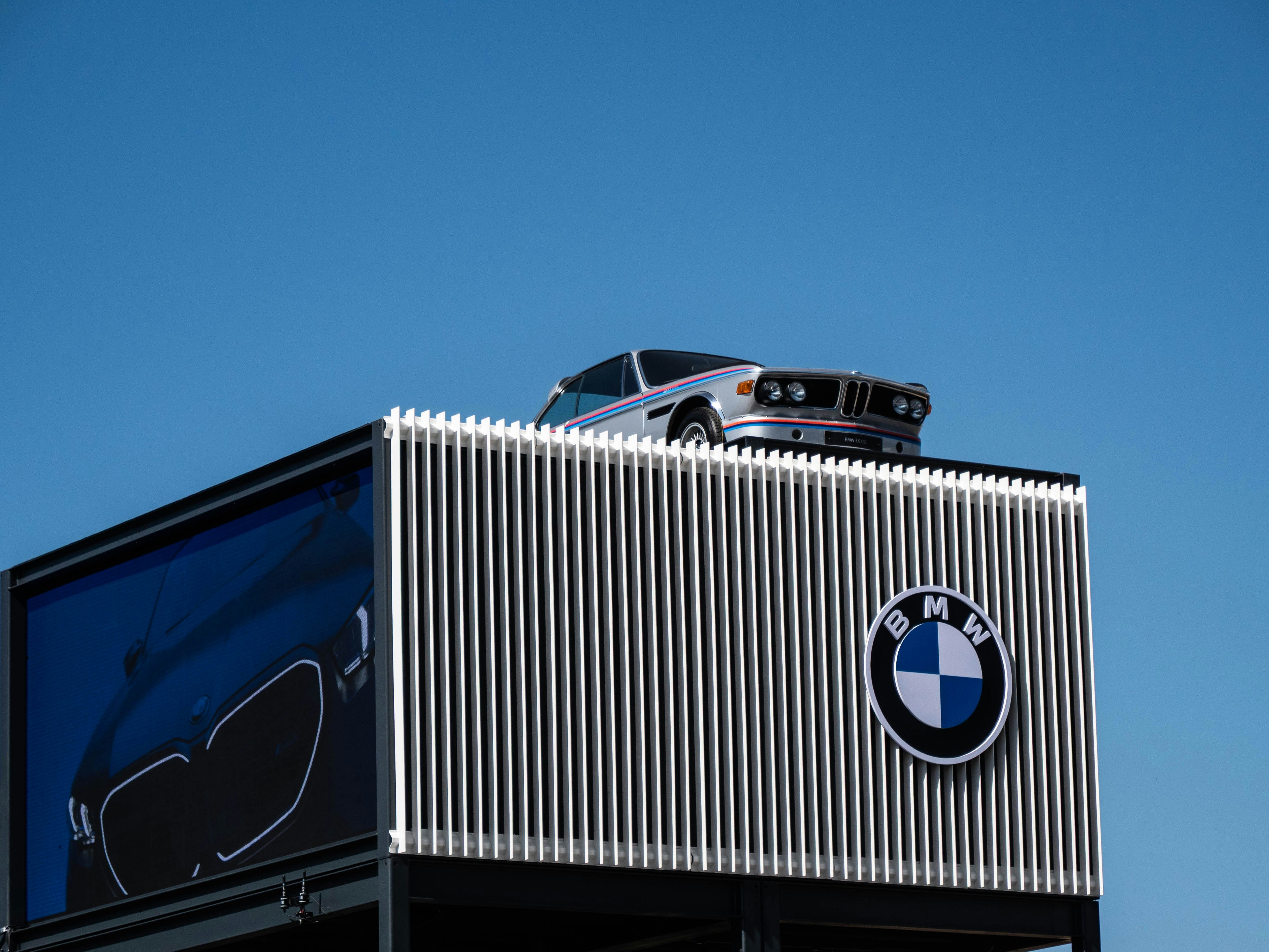 A vintage BMW car sits on roof. | BMW car atop a structure with the logo.