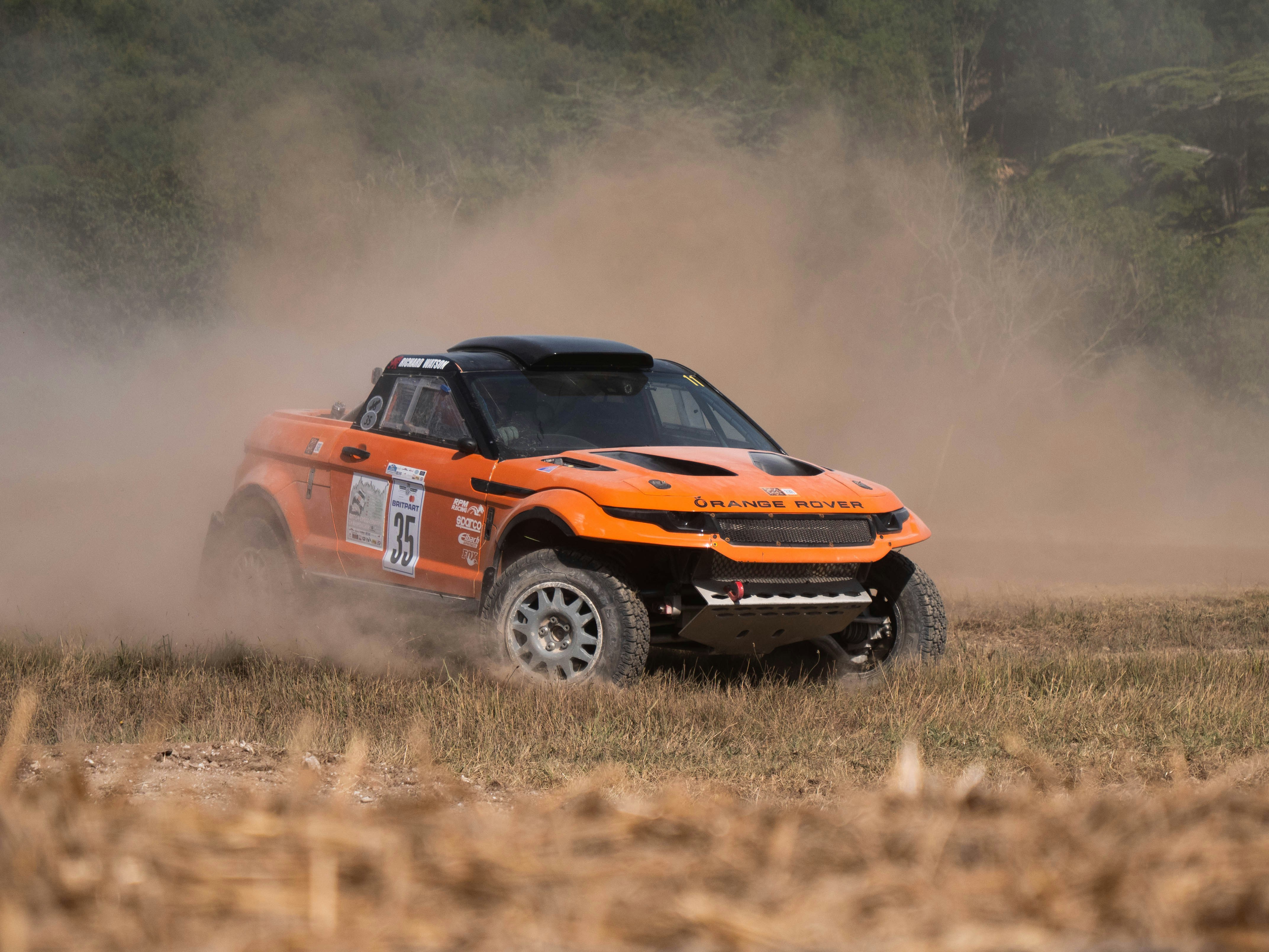 Dust Trail Sprint: Orange Rally Car Carves a Dusty Field Run