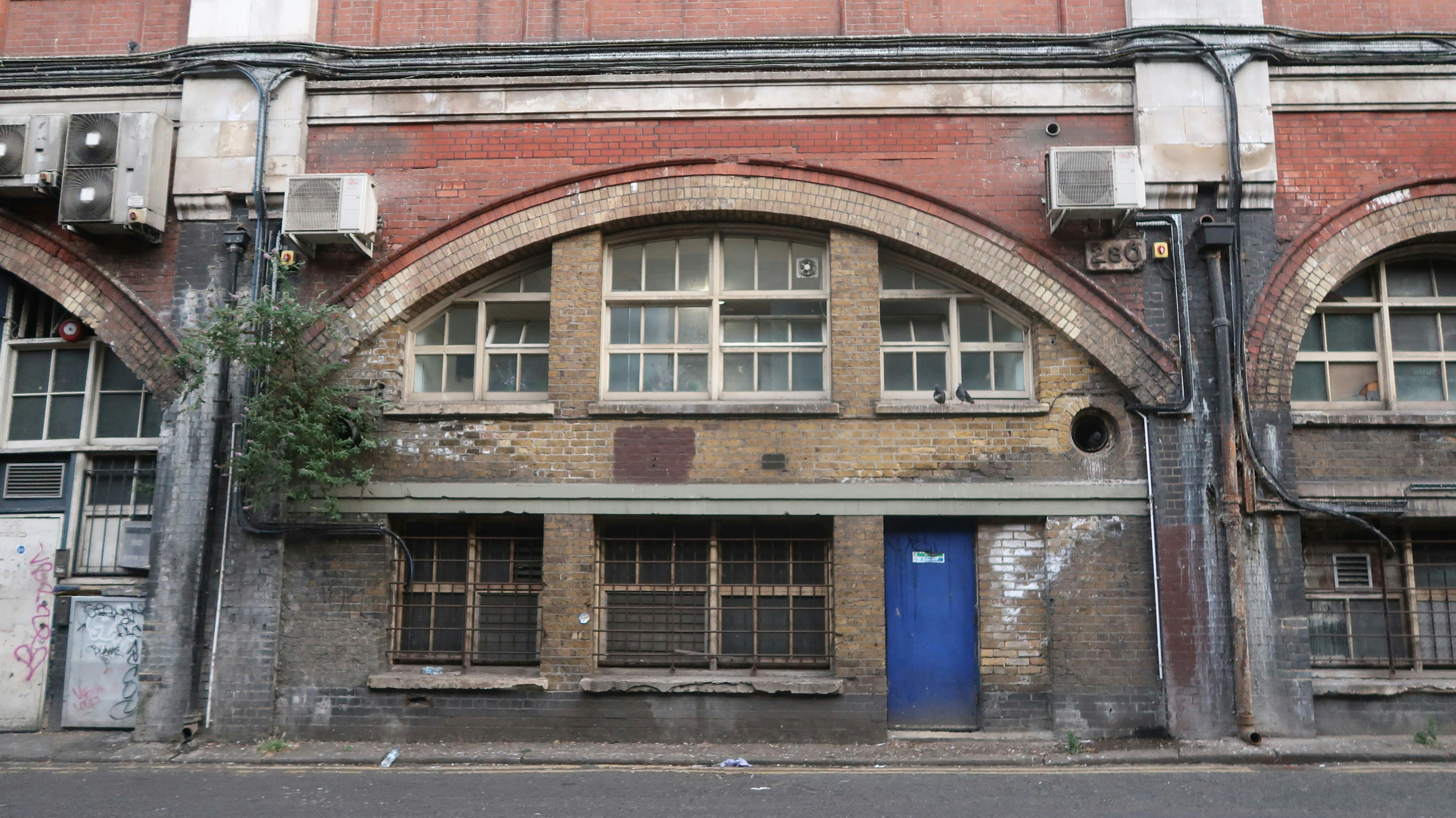 Weathered brick building featuring arched windows and a vibrant blue door, showcasing urban decay and resilience.