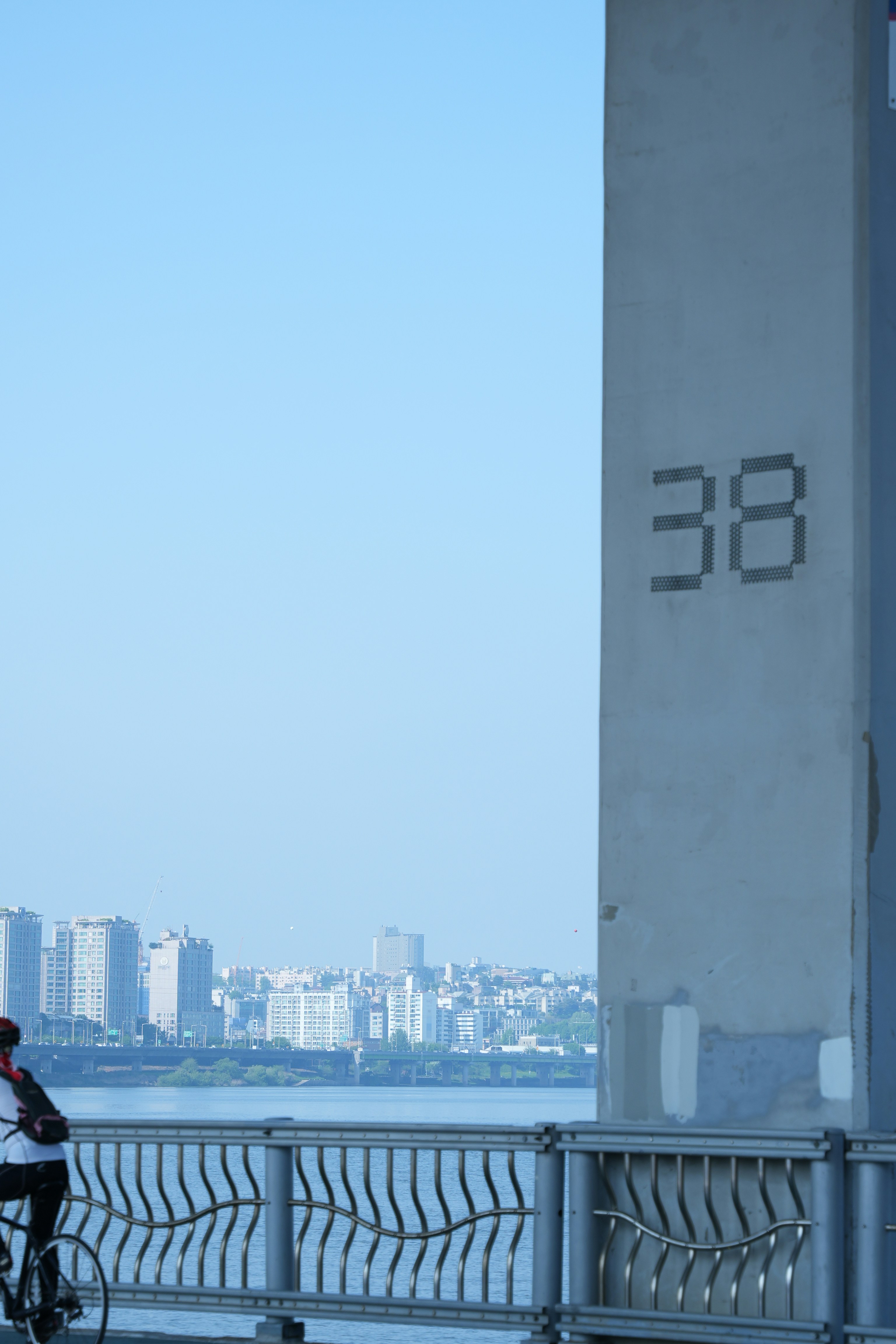 Cyclist on a bridge with city buildings in view.