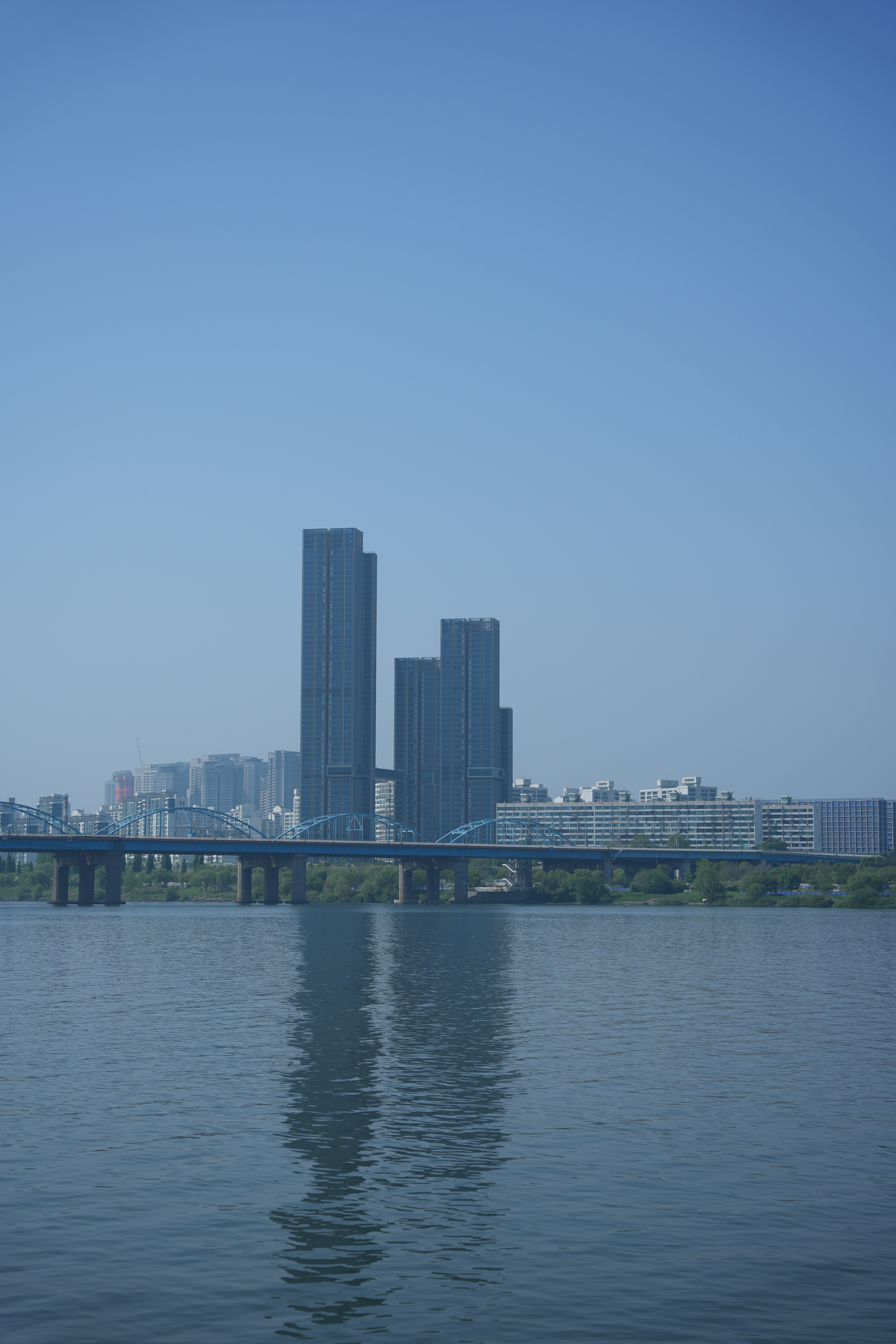 Skyscrapers and a bridge reflect in the water.
