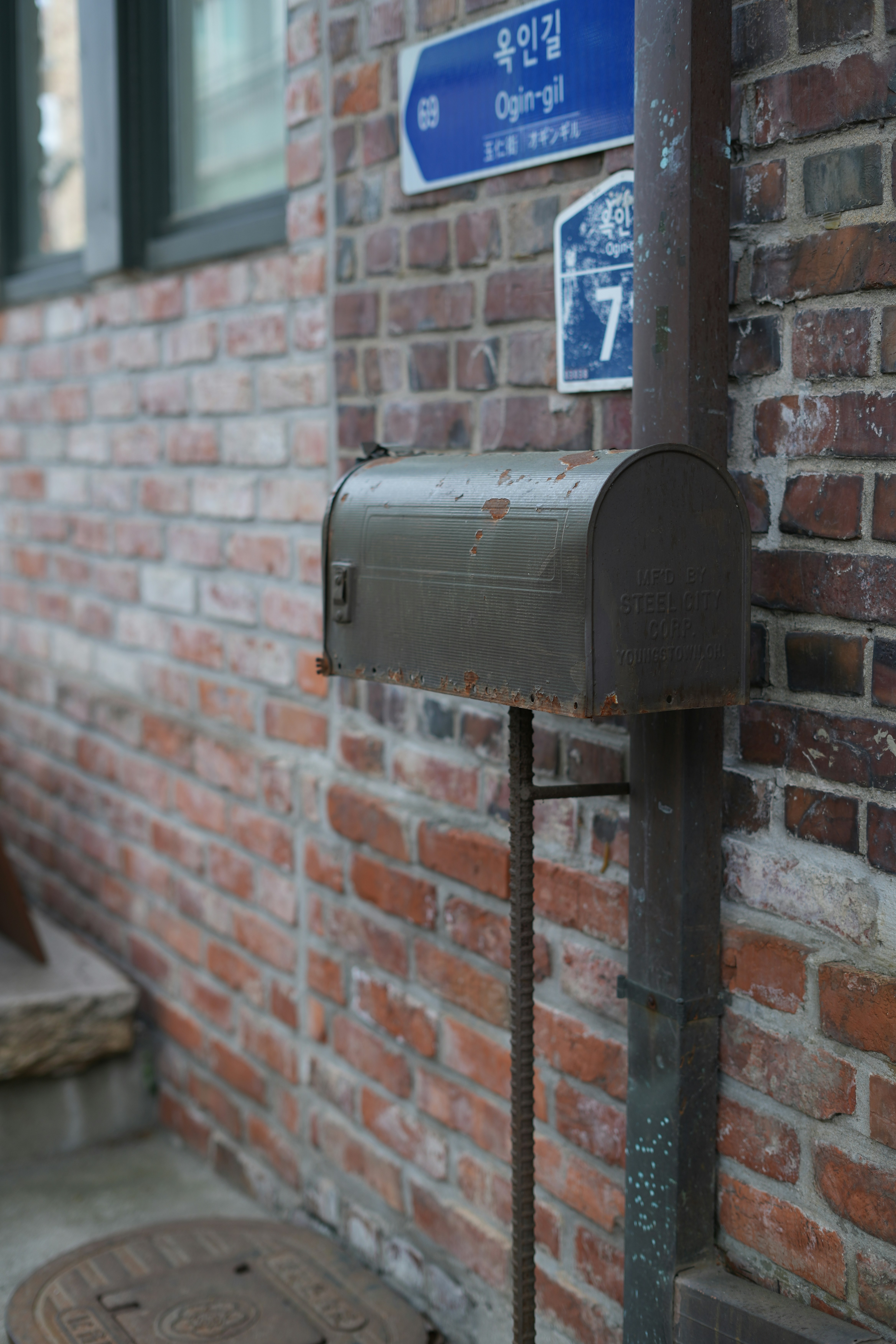 An old mailbox sits beside a brick wall.