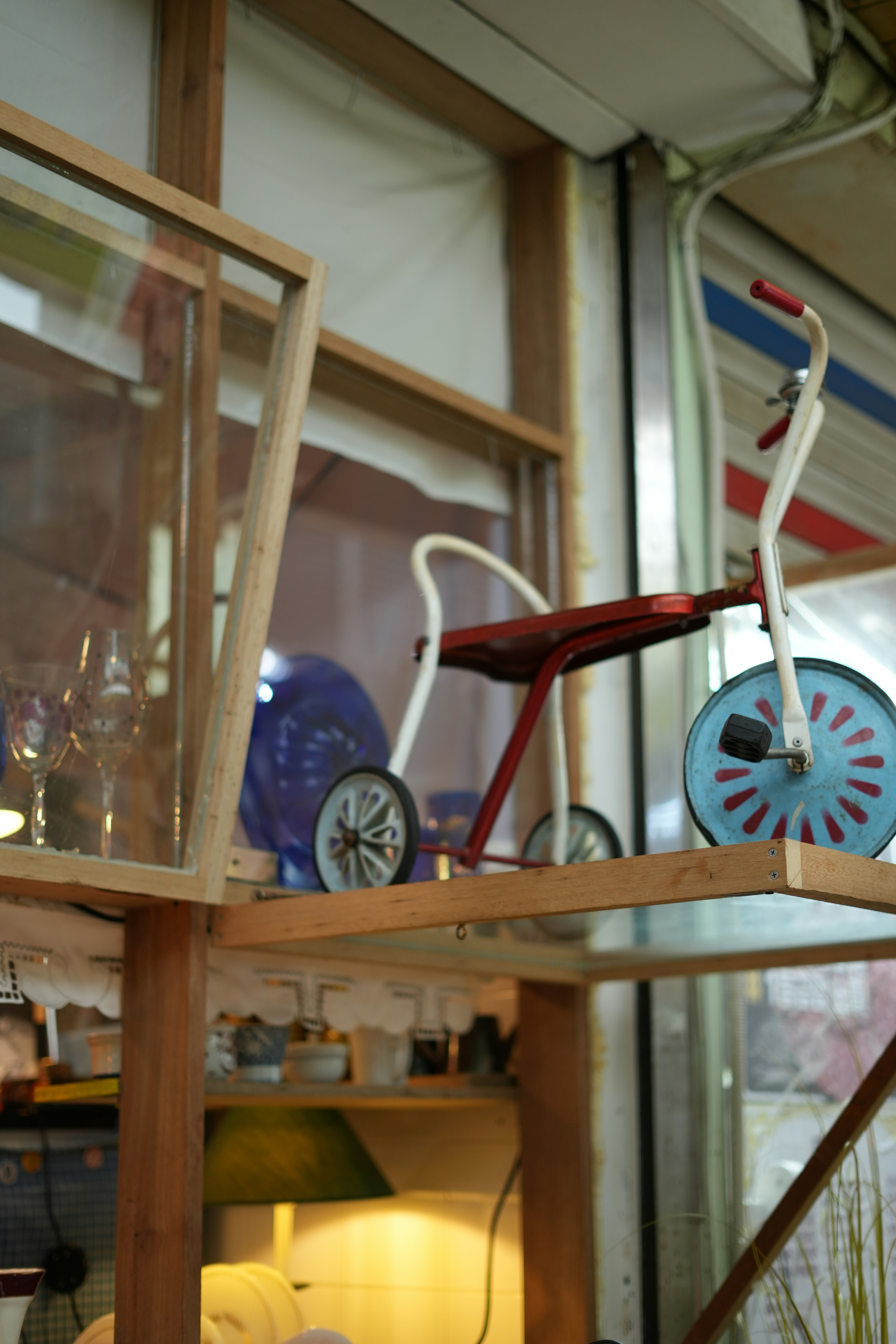 A vintage tricycle showcased on a wooden shelf, surrounded by glassware and colorful decor elements. The scene evokes a sense of playful nostalgia.