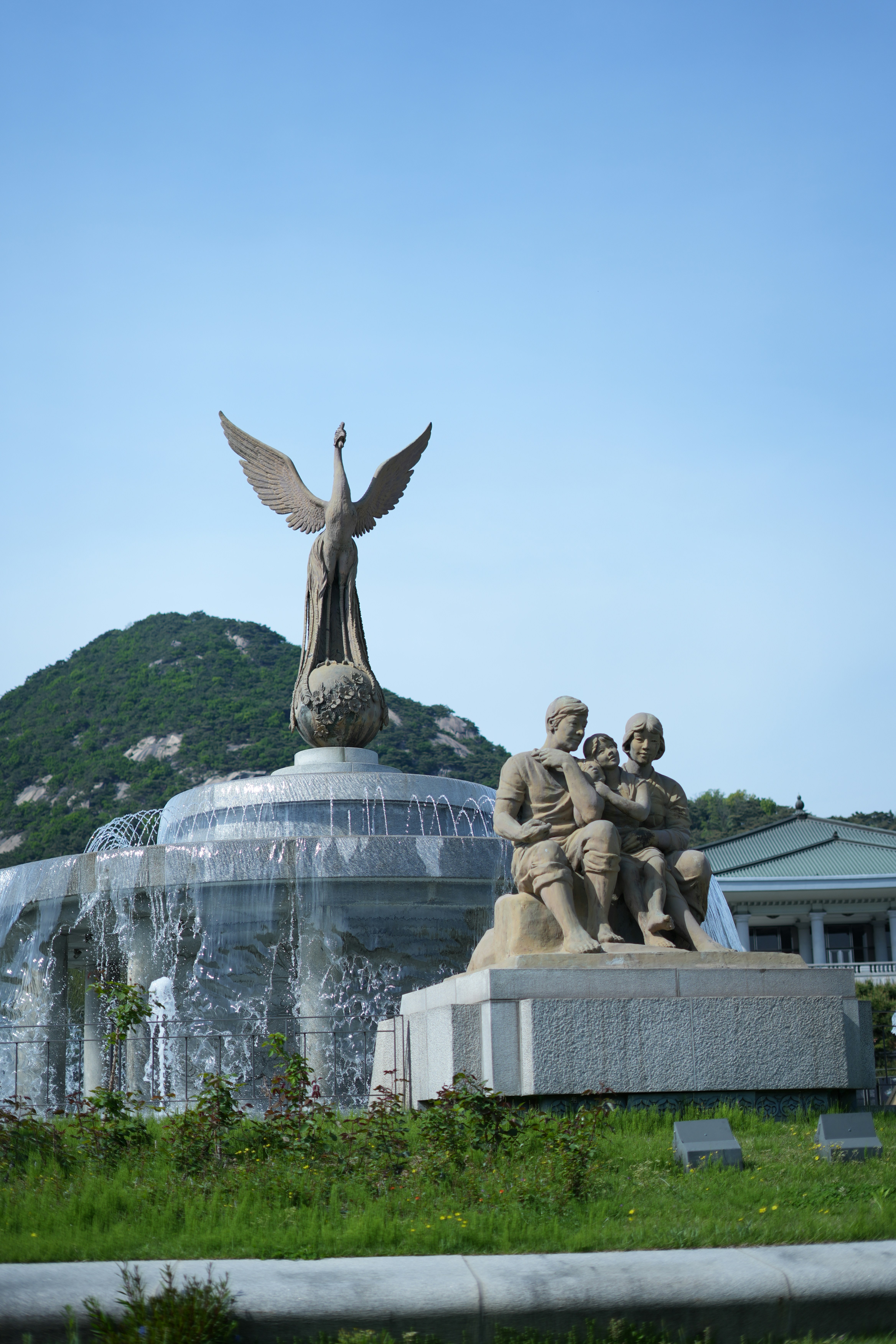 A fountain and statue stand in the sunshine.