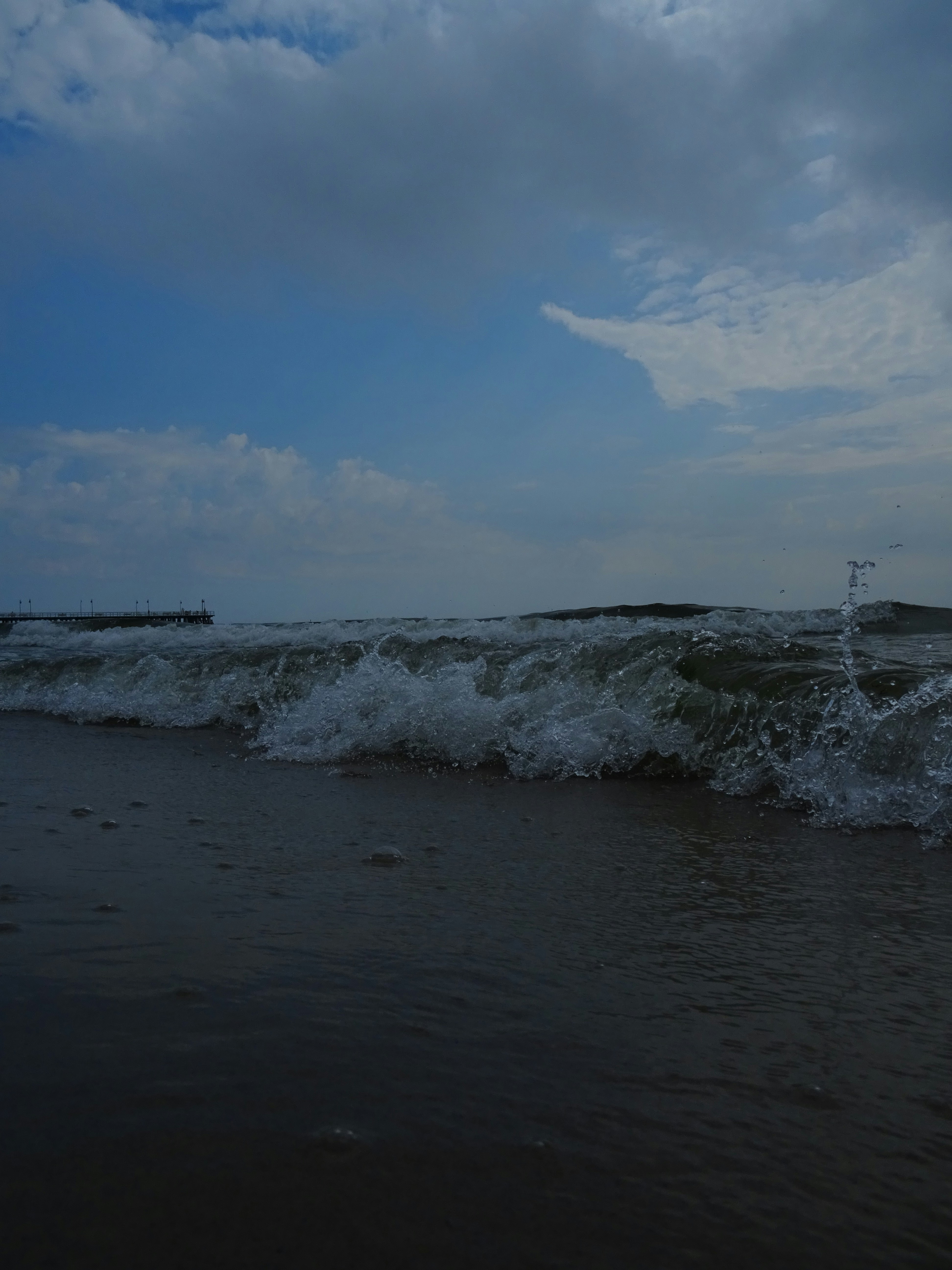 Waves crash on the shore under a cloudy sky.