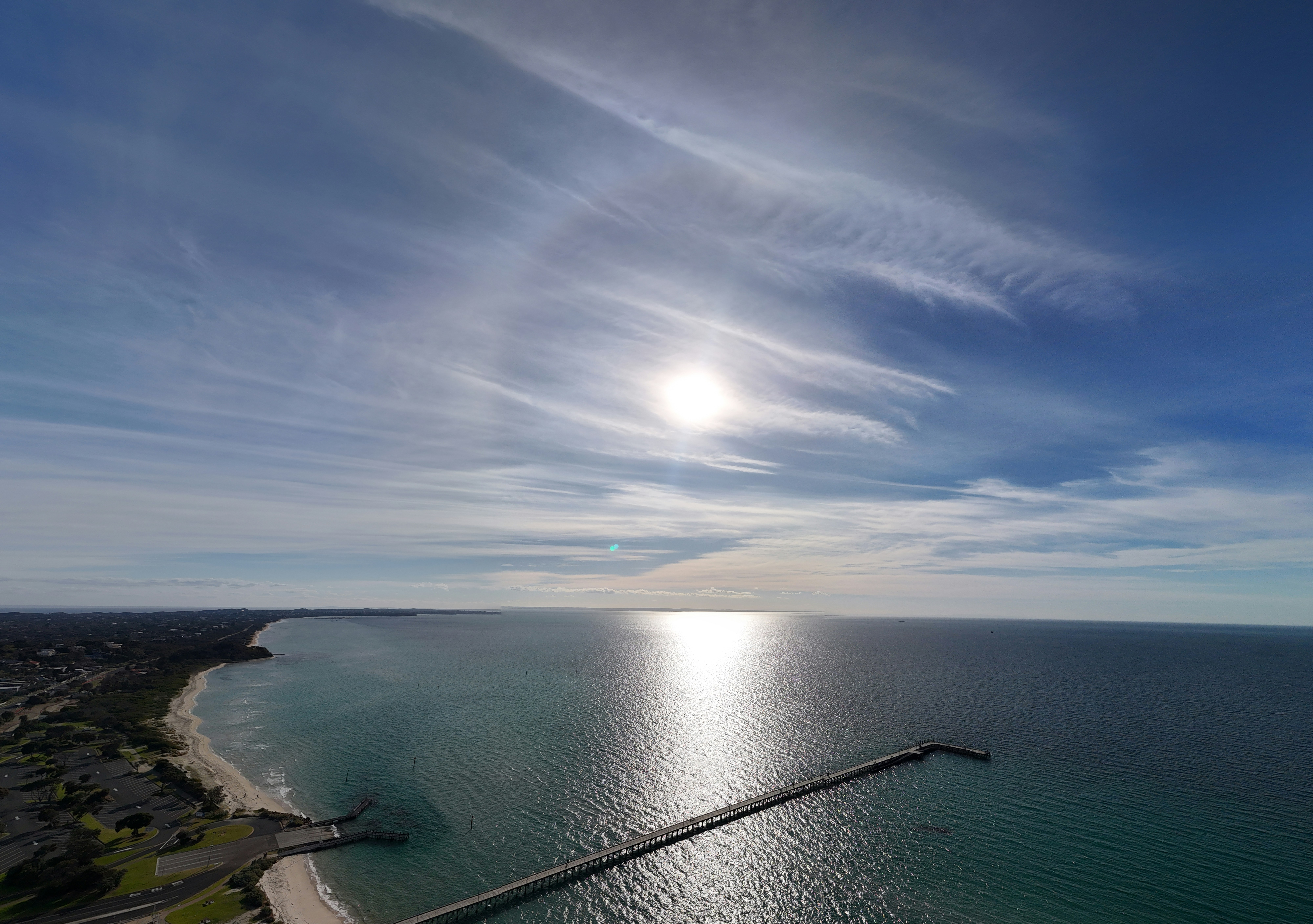 Bright sun reflects on the ocean and pier.