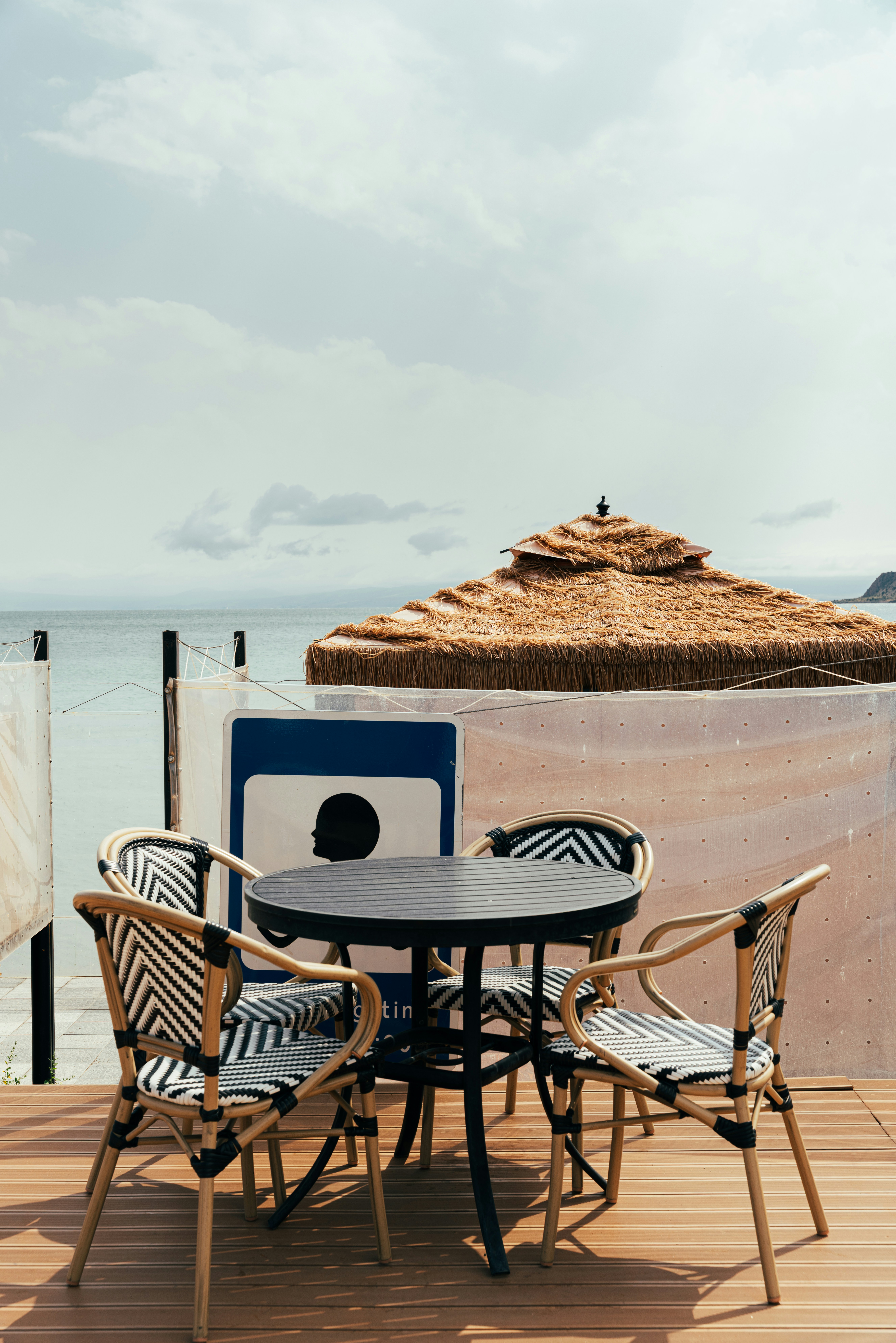 Seaside Café Round Table Beneath a Straw Thatch, Framing a Calm Ocean View