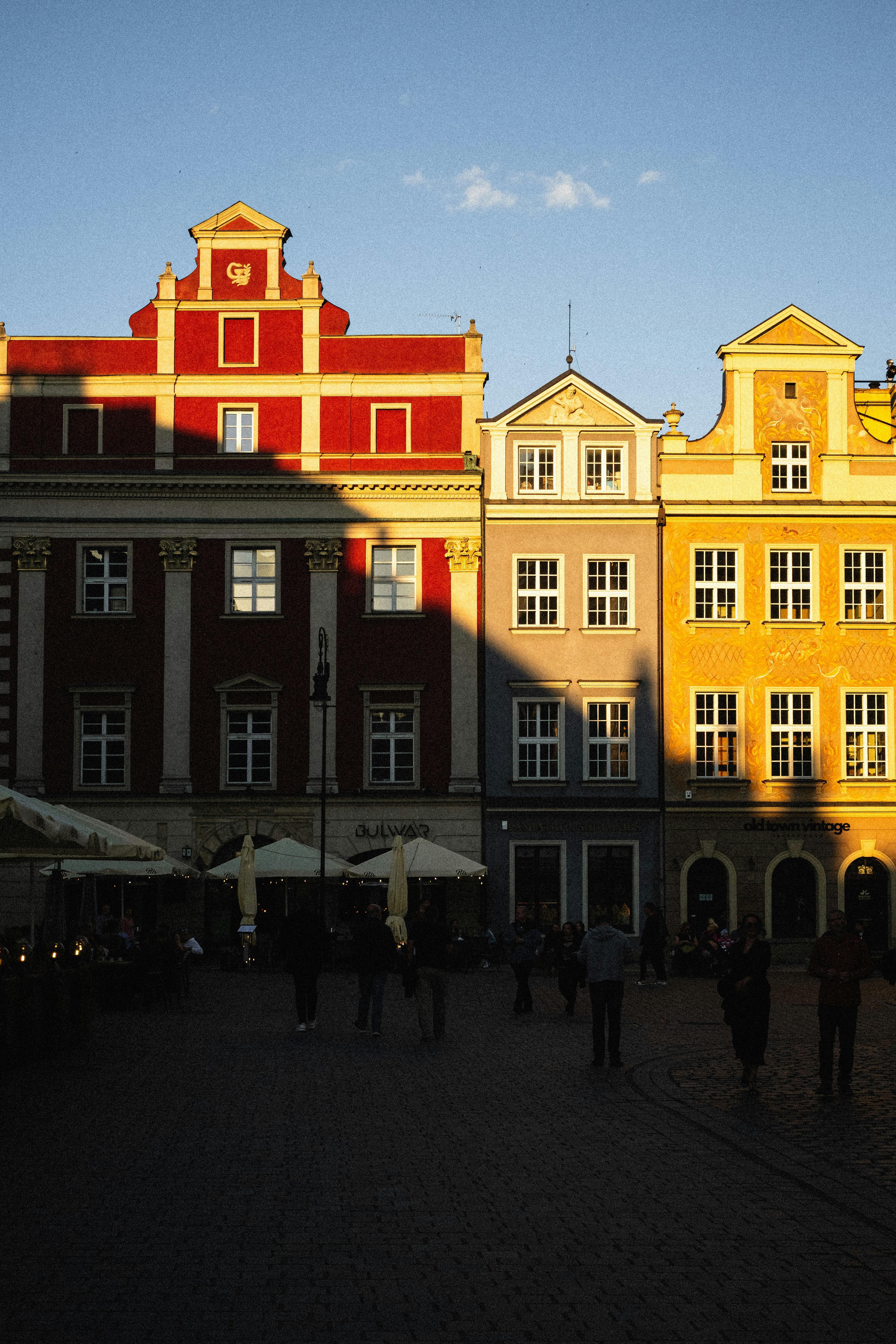 Historic buildings adorned with vibrant colors and intricate details, cast dramatic shadows as the sun sets in a bustling square.