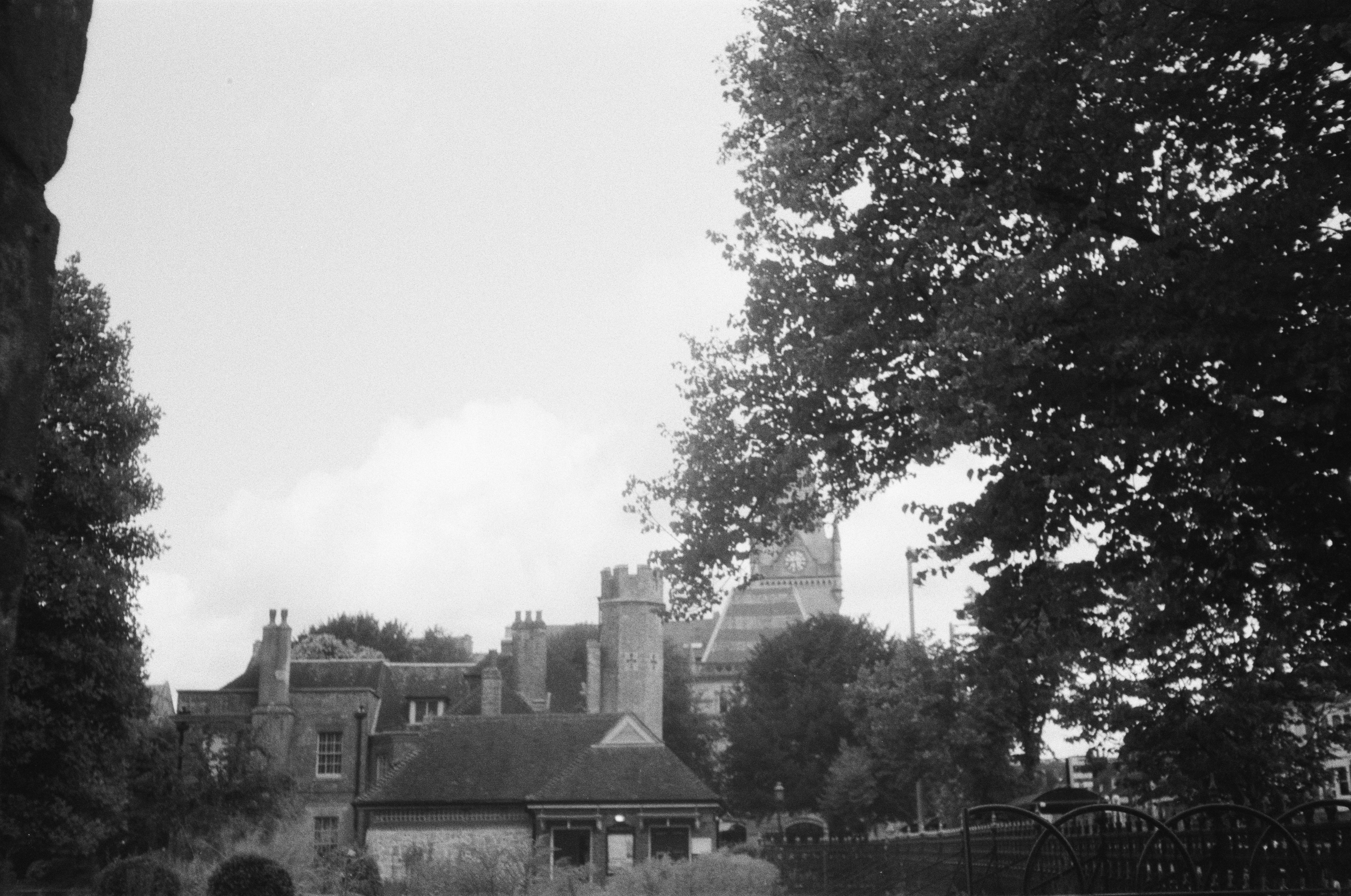 Historic buildings framed by lush greenery in a serene park setting. Soft clouds drift above, enhancing the tranquil atmosphere.