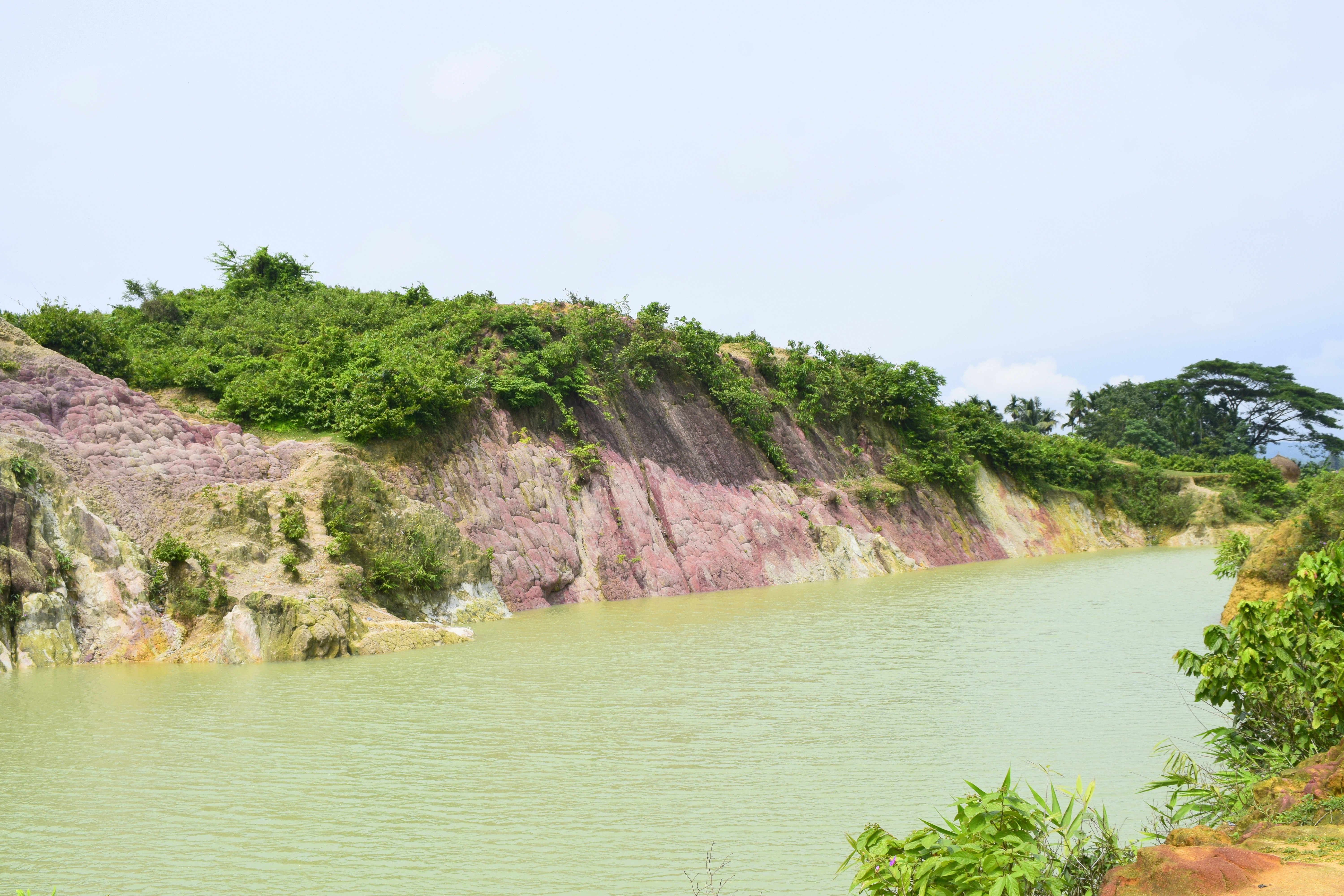 China Matir Pahar, a hidden gem in Netrokona, Bangladesh, stuns with its surreal white clay hills and nature-sculpted beauty. | Scenic view of water and rocky hillsides.