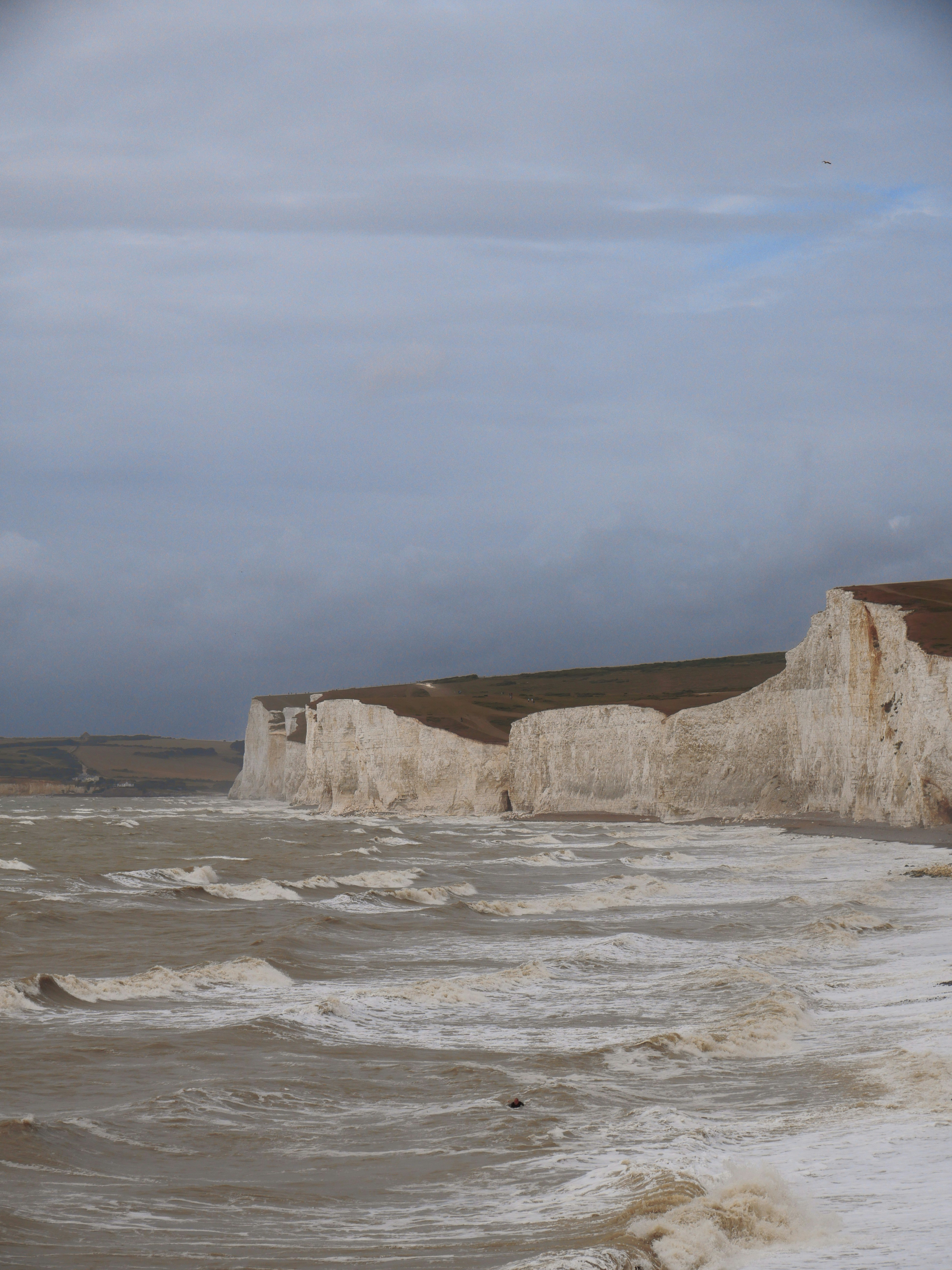 Die dramatischen weißen Kreidefelsen der Seven Sisters in Eastbourne, Großbritannien, an einem stürmischen Tag, mit rauen Wellen, die gegen die Küste schlagen. Ein beeindruckendes Bild der natürlichen Schönheit und Kraft der britischen Küste. | Waves crash against white cliffs in stormy weather.