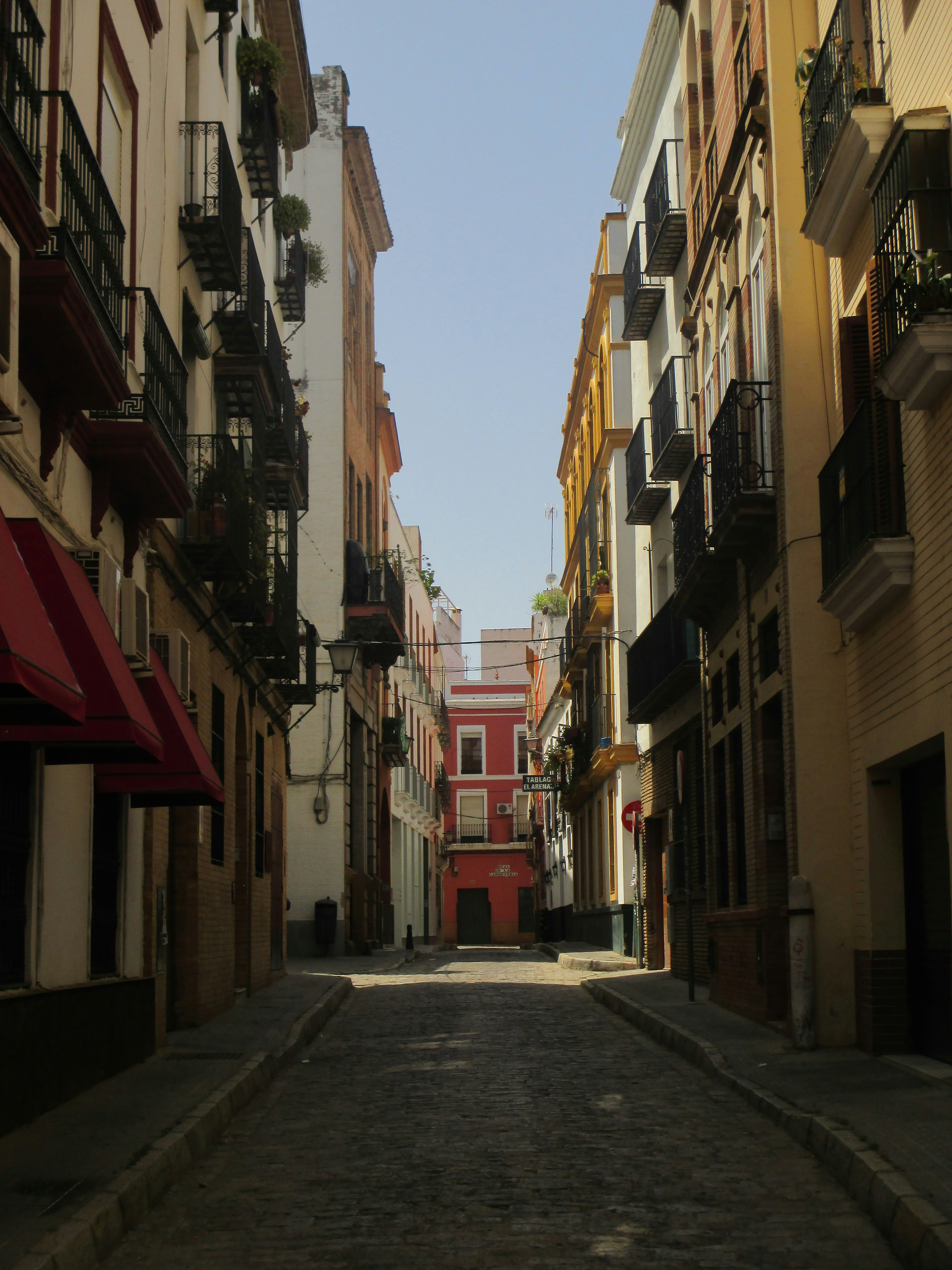 Sunny colourful street | Narrow street lined with buildings under a bright sky.