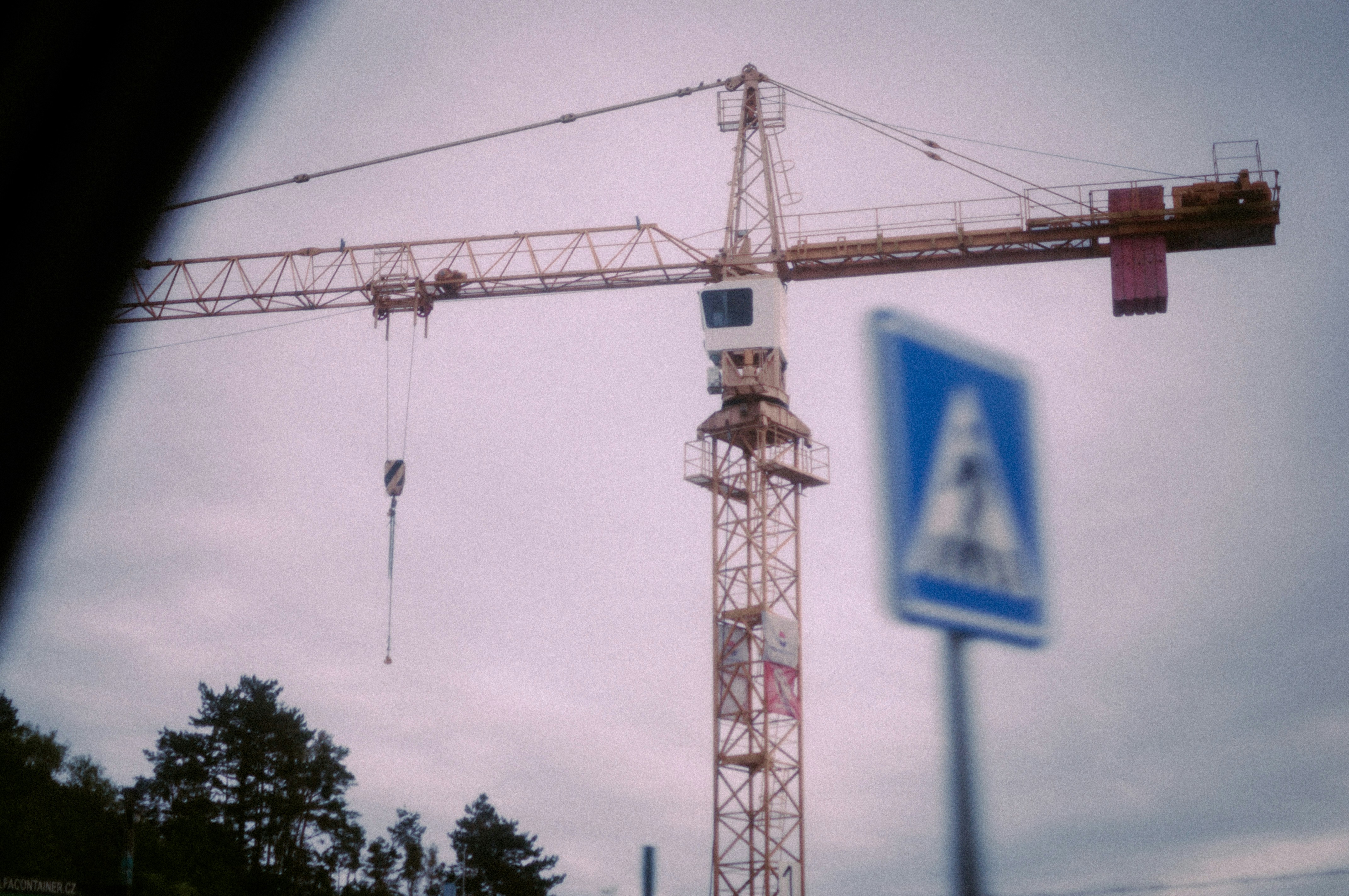 A construction crane stands tall beside a pedestrian sign.