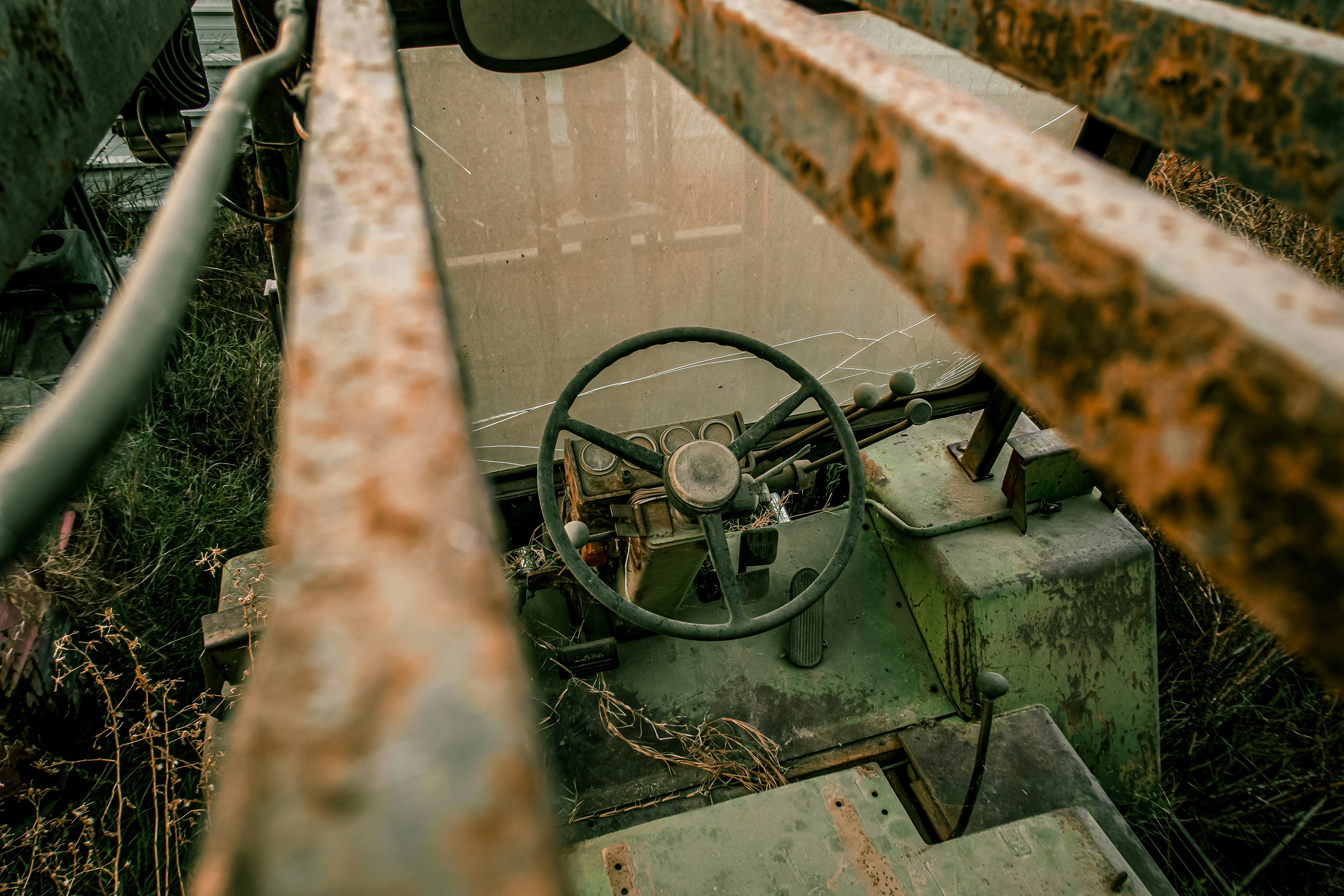 A view from above of the rusty remains of a forklift in a junkyard. | Rusty steering wheel inside an old vehicle.
