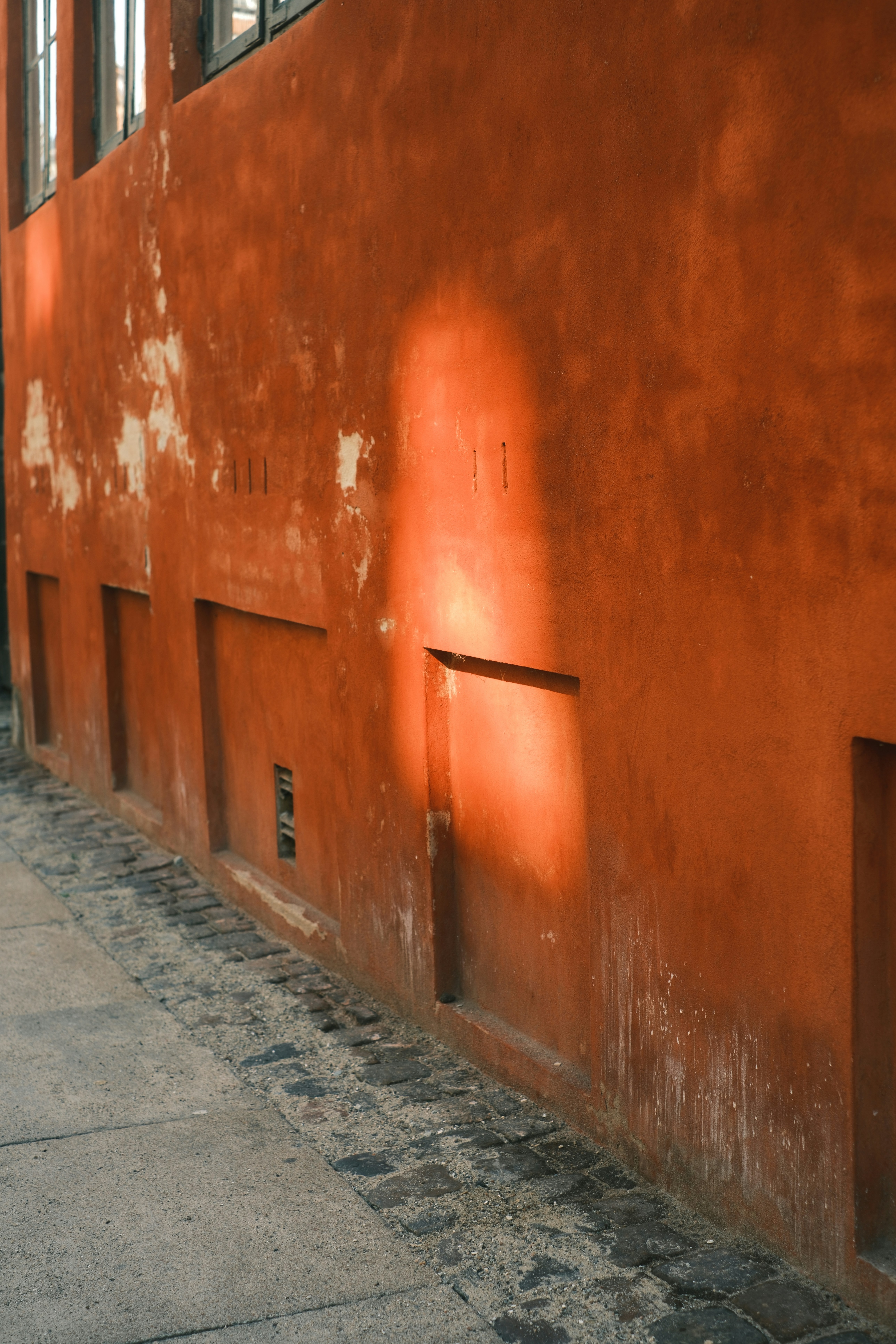 Evening dappled sunlight on an old wall in the streets of Copenhagen | Sunlight illuminates a weathered, reddish-orange wall.