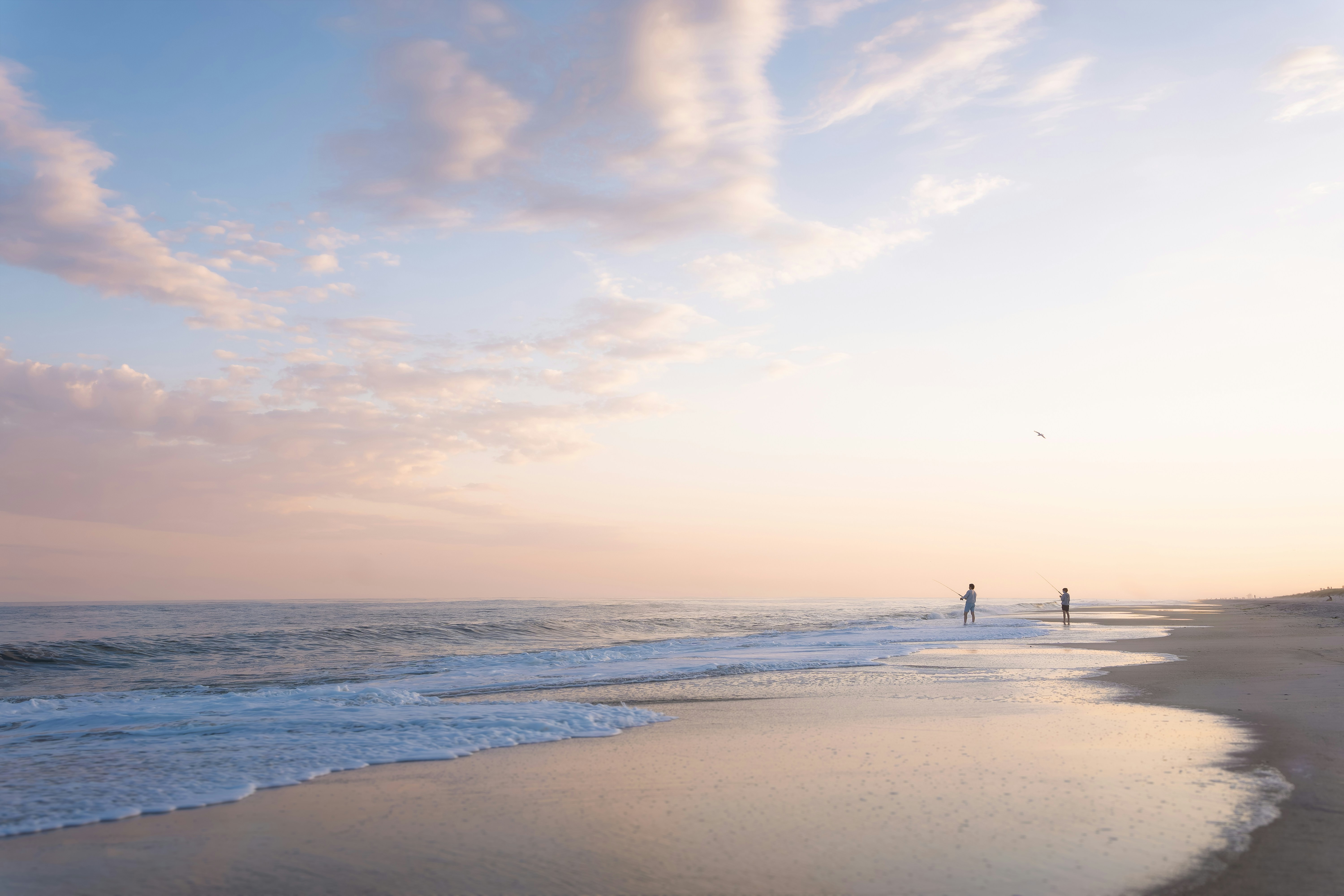 A father and son fish off the beach at sunset.
