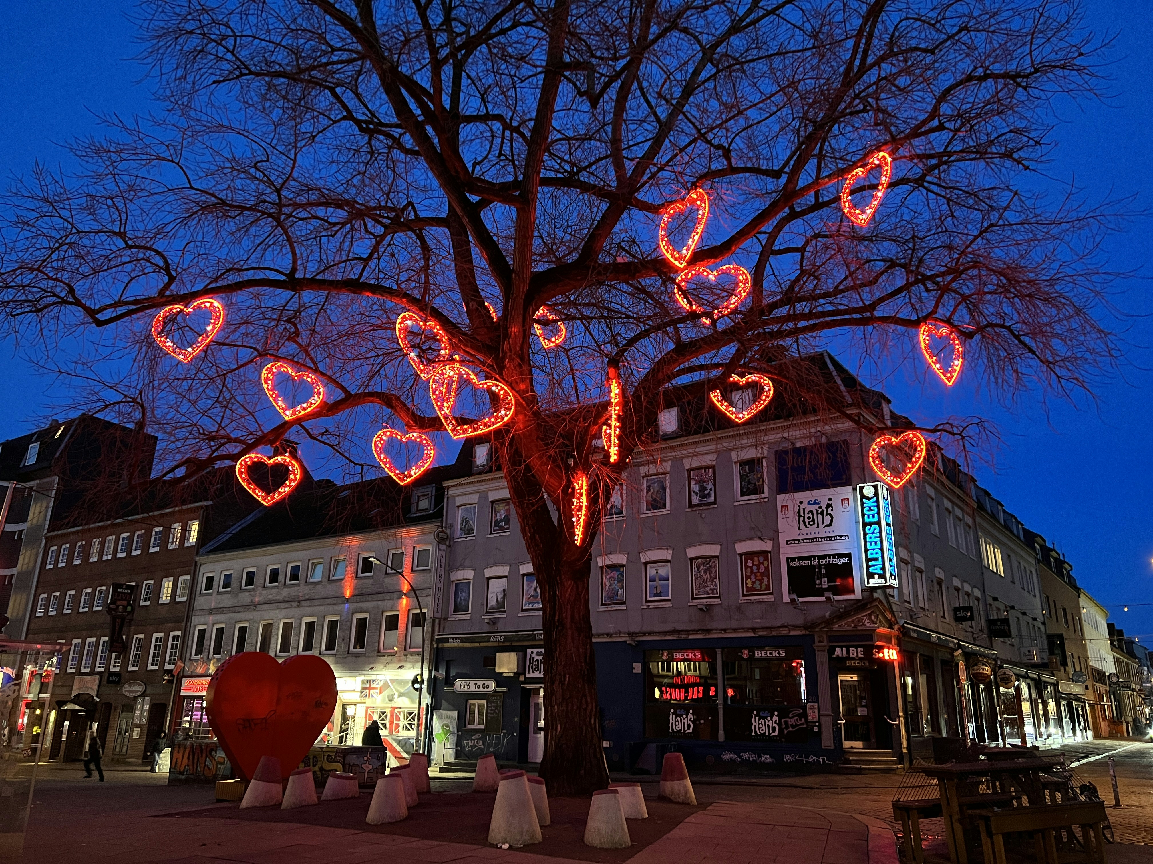 A vibrant tree is illuminated by twinkling red lights against a bustling Hamburg backdrop, capturing the city's energetic atmosphere. | A tree is decorated with valentine's day lights.