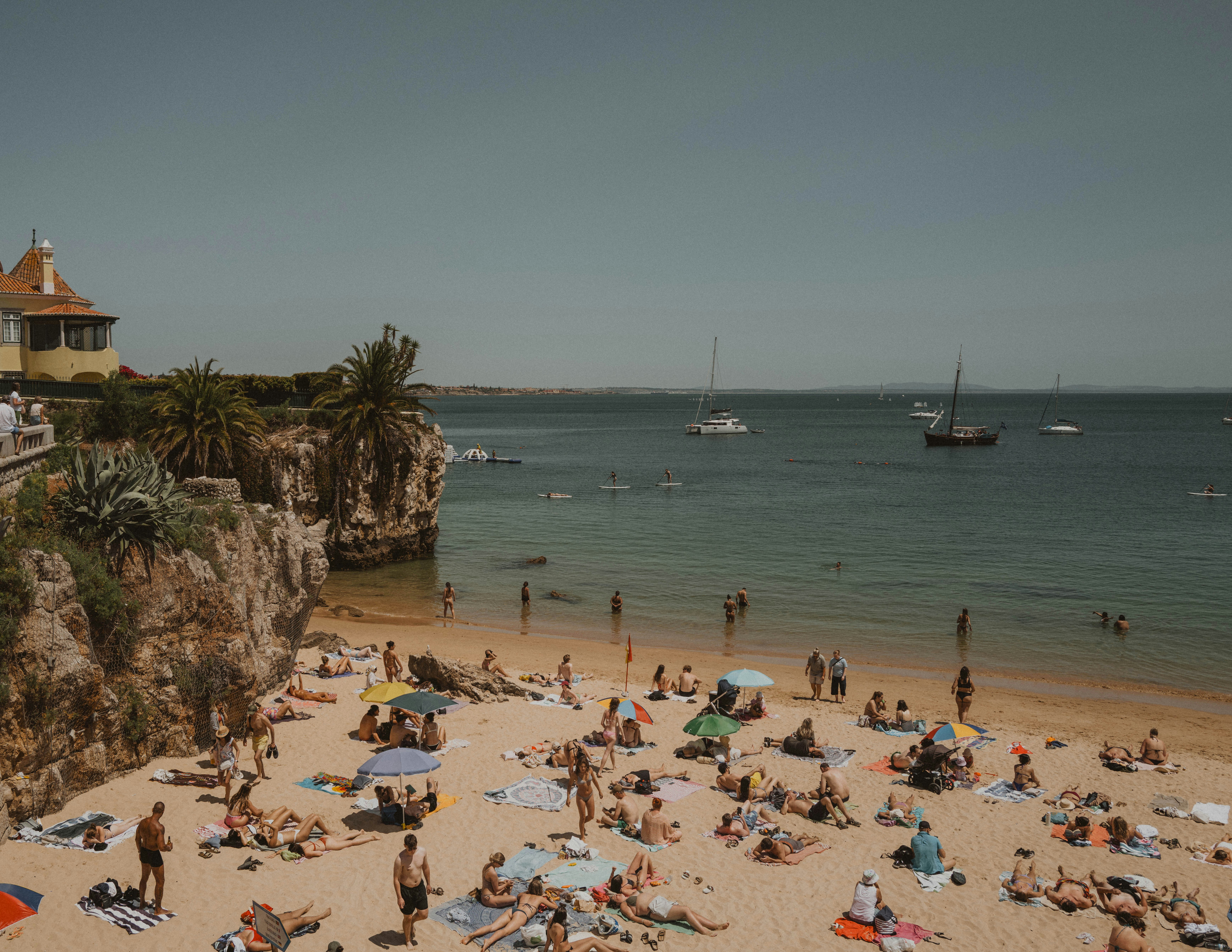 Sunlit Costa: Beachgoers, Cliffside Villa, and calm sea