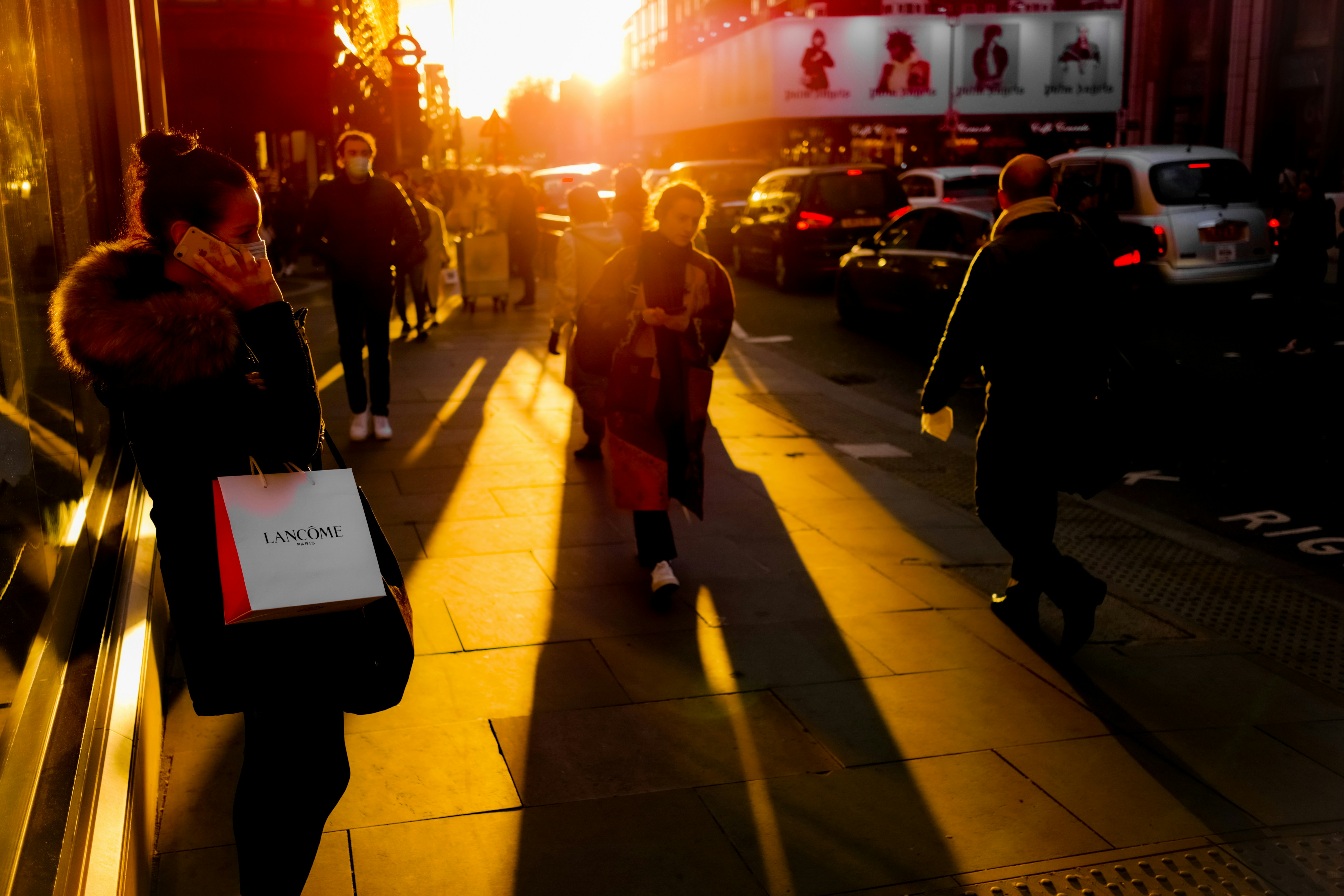 People walk down a city street at sunset.