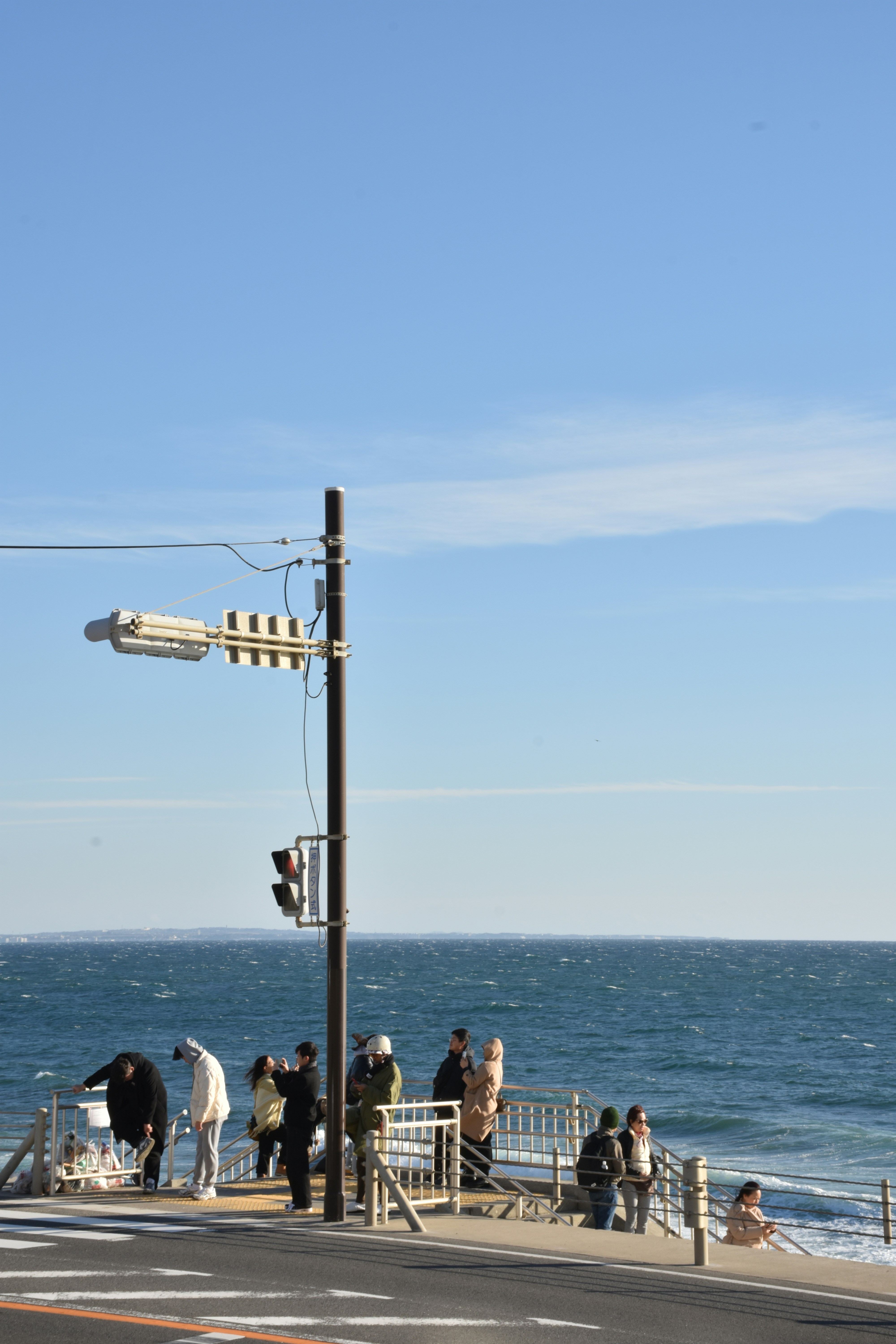 Visitors enjoying a sunny day at the seaside, with waves crashing against the shore and a clear blue sky overhead.