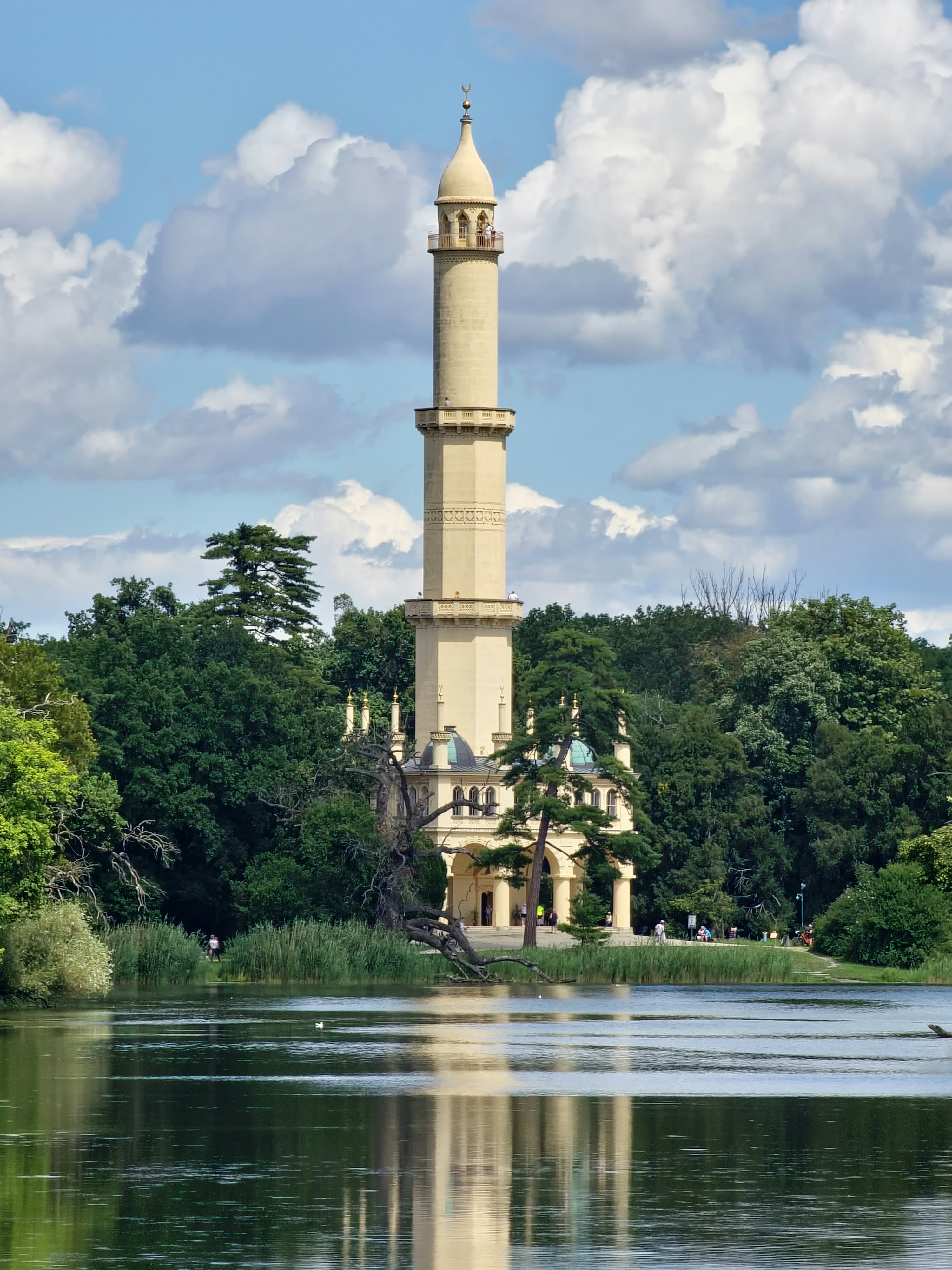 Minaret in nature | A tall minaret towers over a lake.