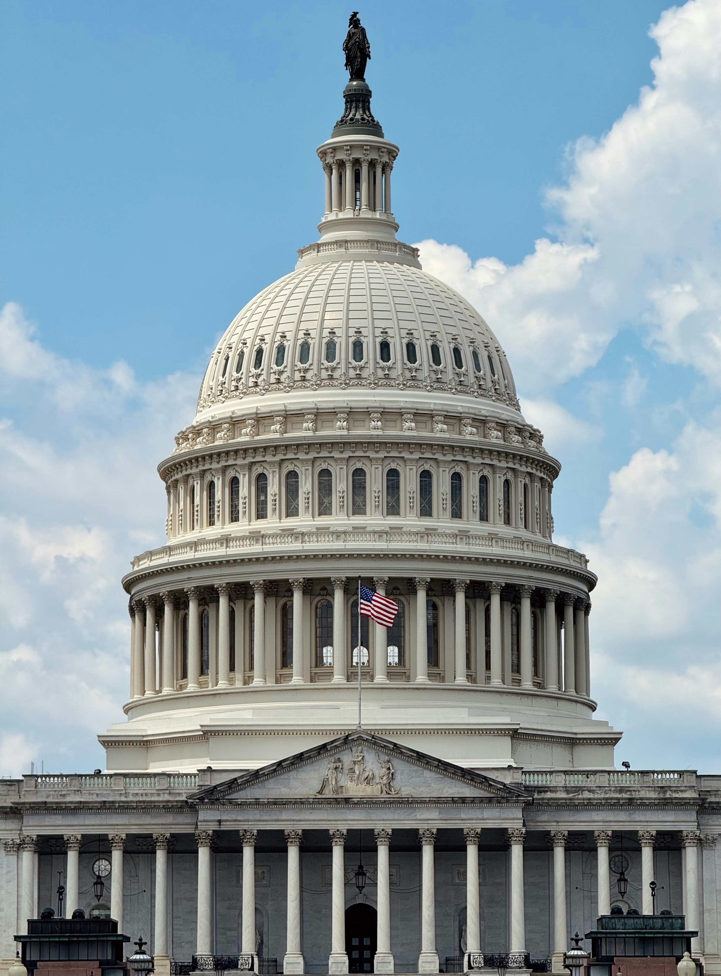The iconic dome of the U.S. Capitol building stands majestically against a backdrop of fluffy clouds, showcasing its architectural grandeur.