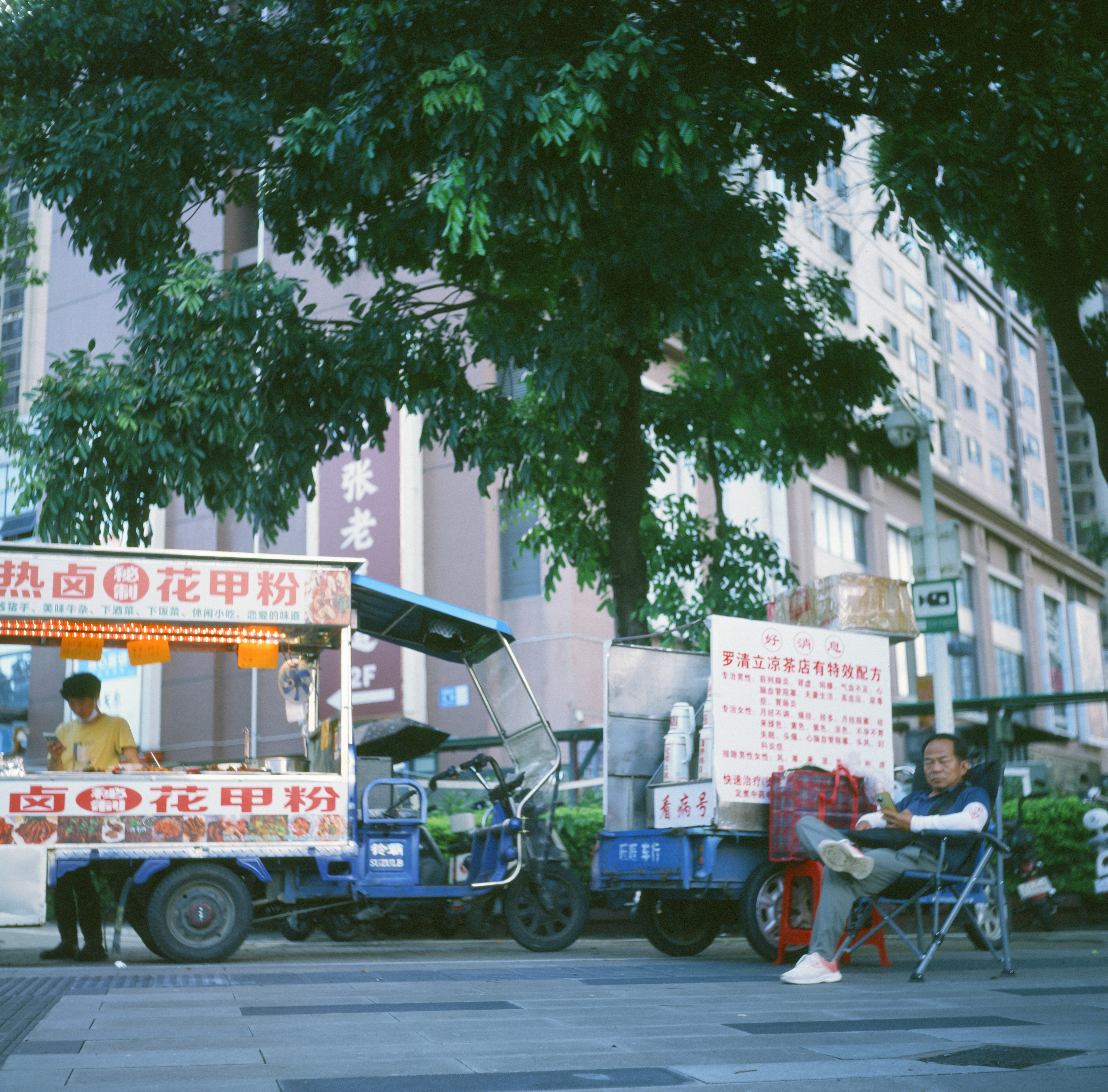 Along the streets, small stalls offer a variety of snacks and refreshing herbal teas, adding a touch of authentic local flavor to everyday life. | A food cart sits on a busy street.