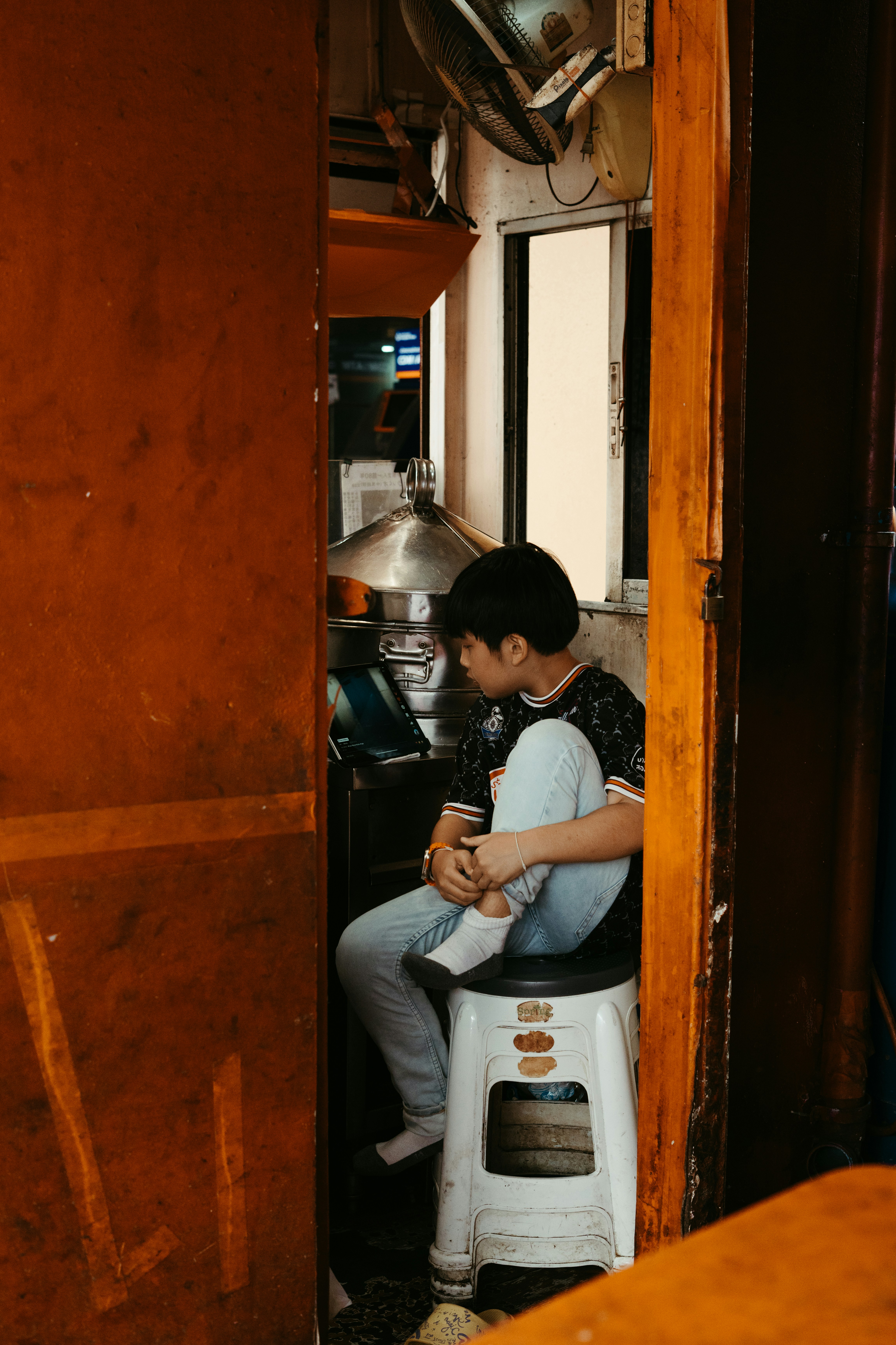 A boy sits inside a small stall.